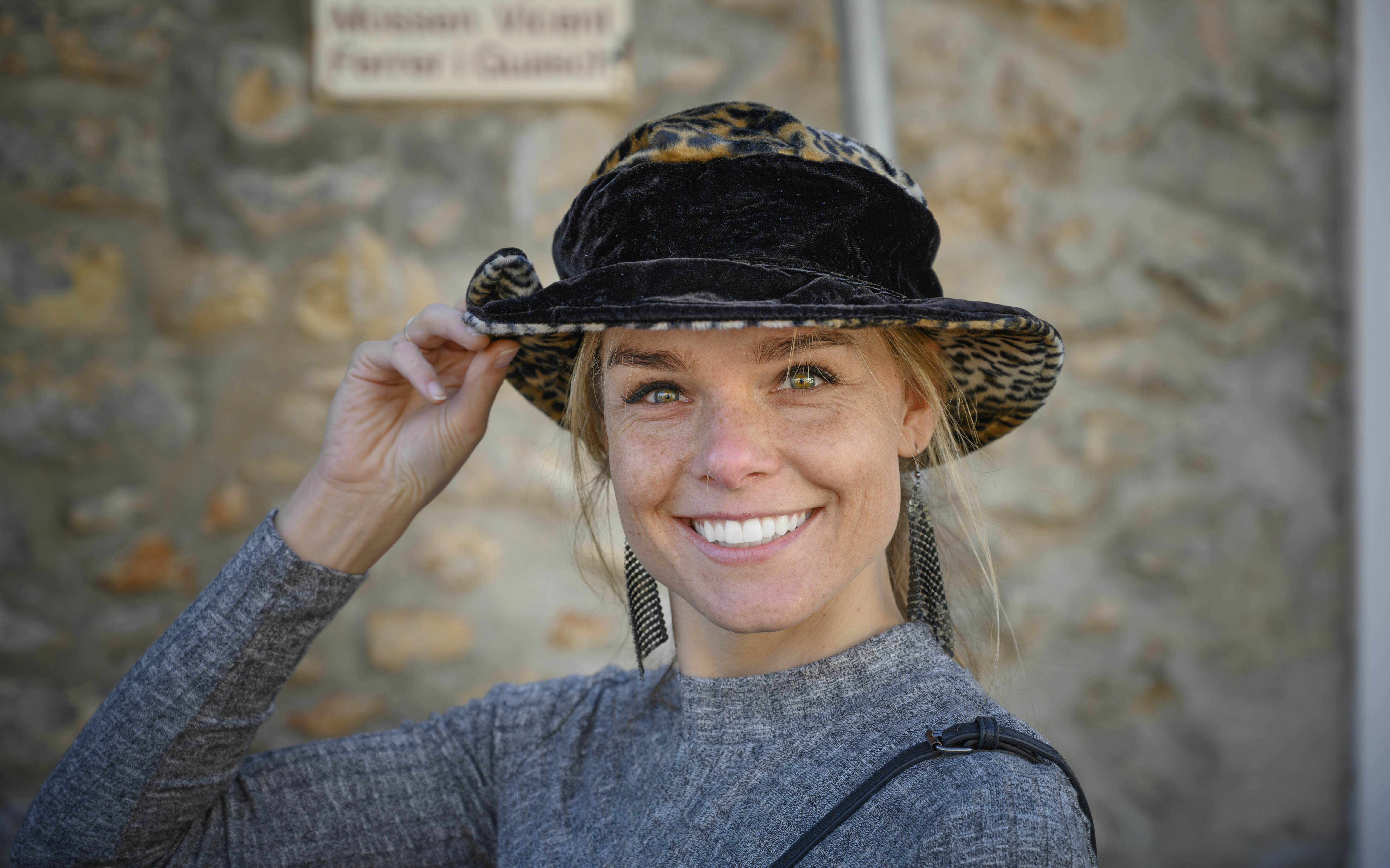 Hat, Hand, and a Sunlit Smile: Portrait by a Weathered Wall
