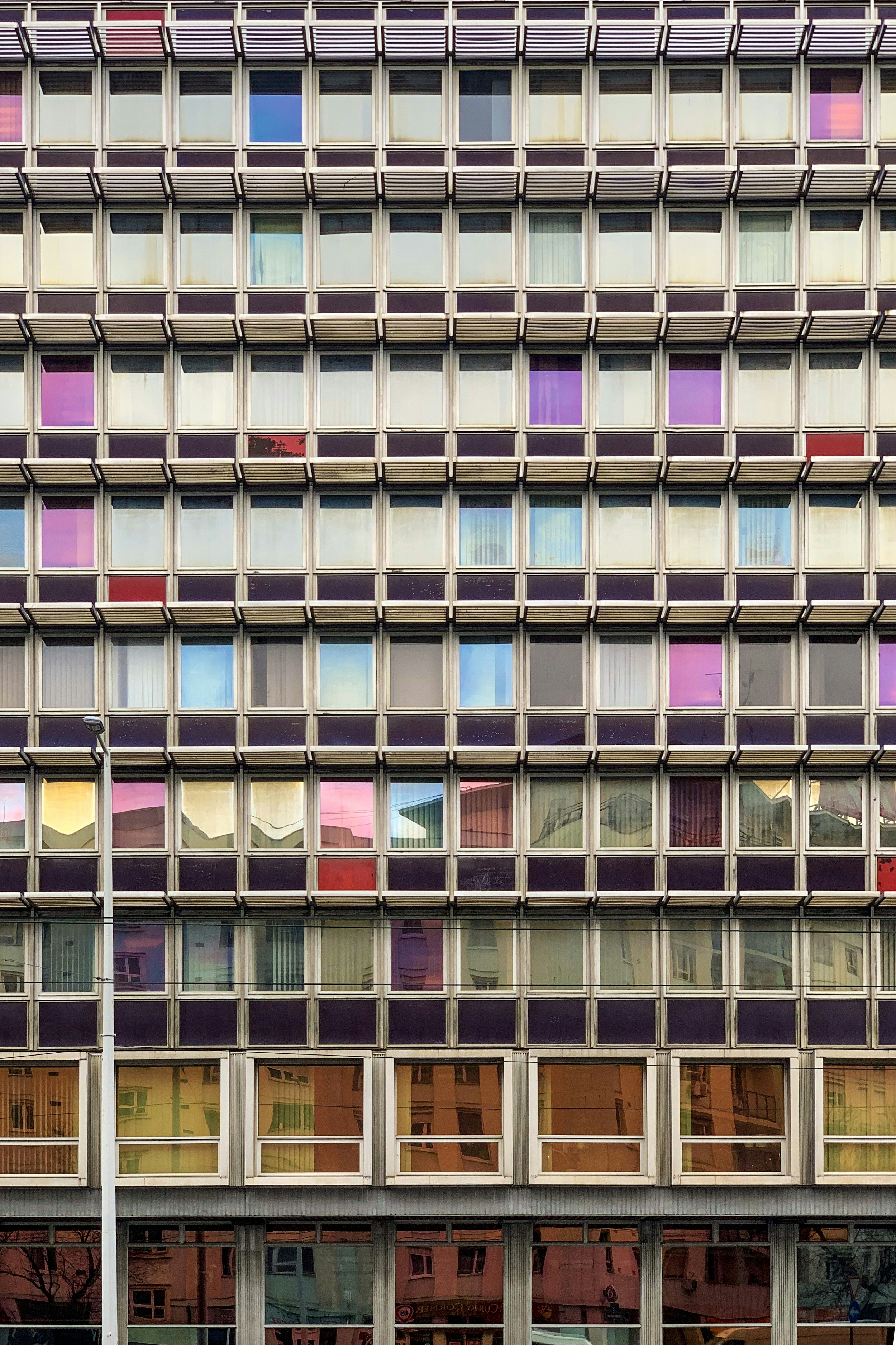 A geometric building facade featuring a grid of colorful windows reflecting the urban environment. The interplay of light and color creates a vibrant visual tapestry.