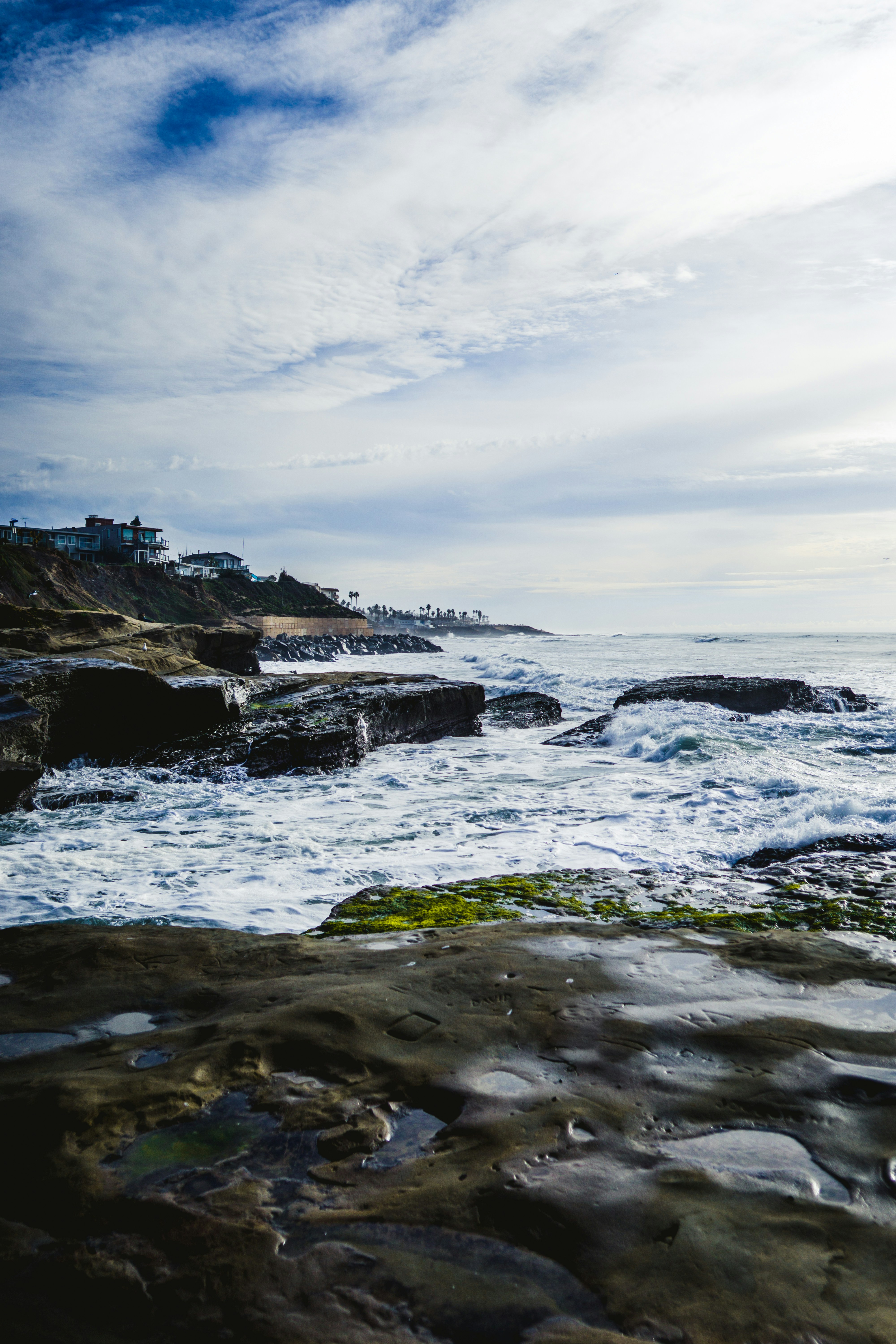 Waves crash against rocky shore under a cloudy sky, highlighting the coastal landscape's natural beauty.