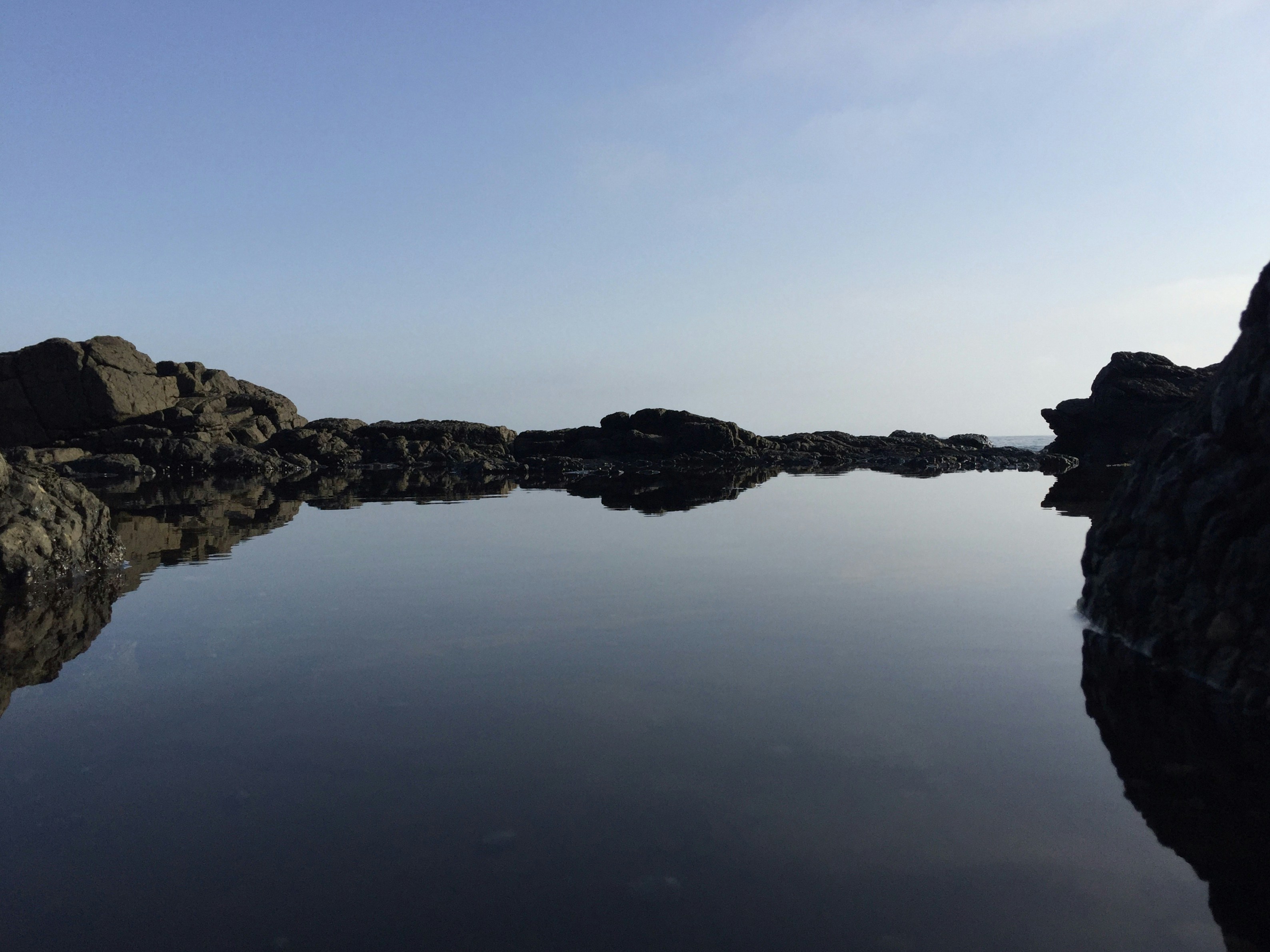 Still water reflecting rocky outcrops under a clear blue sky.