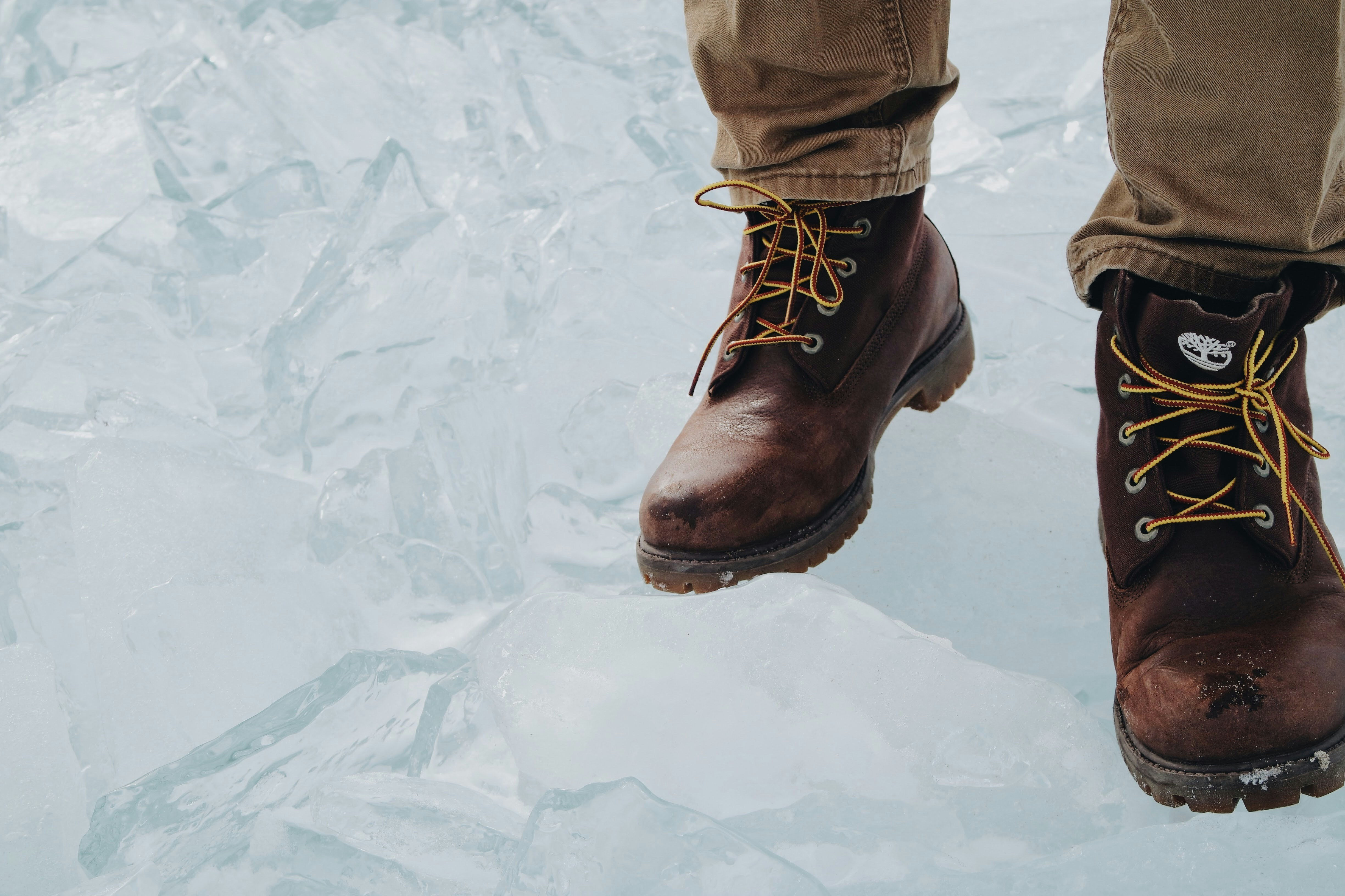 Brown leather boots standing on a cracked ice surface, highlighting the contrast between the footwear and the icy backdrop.