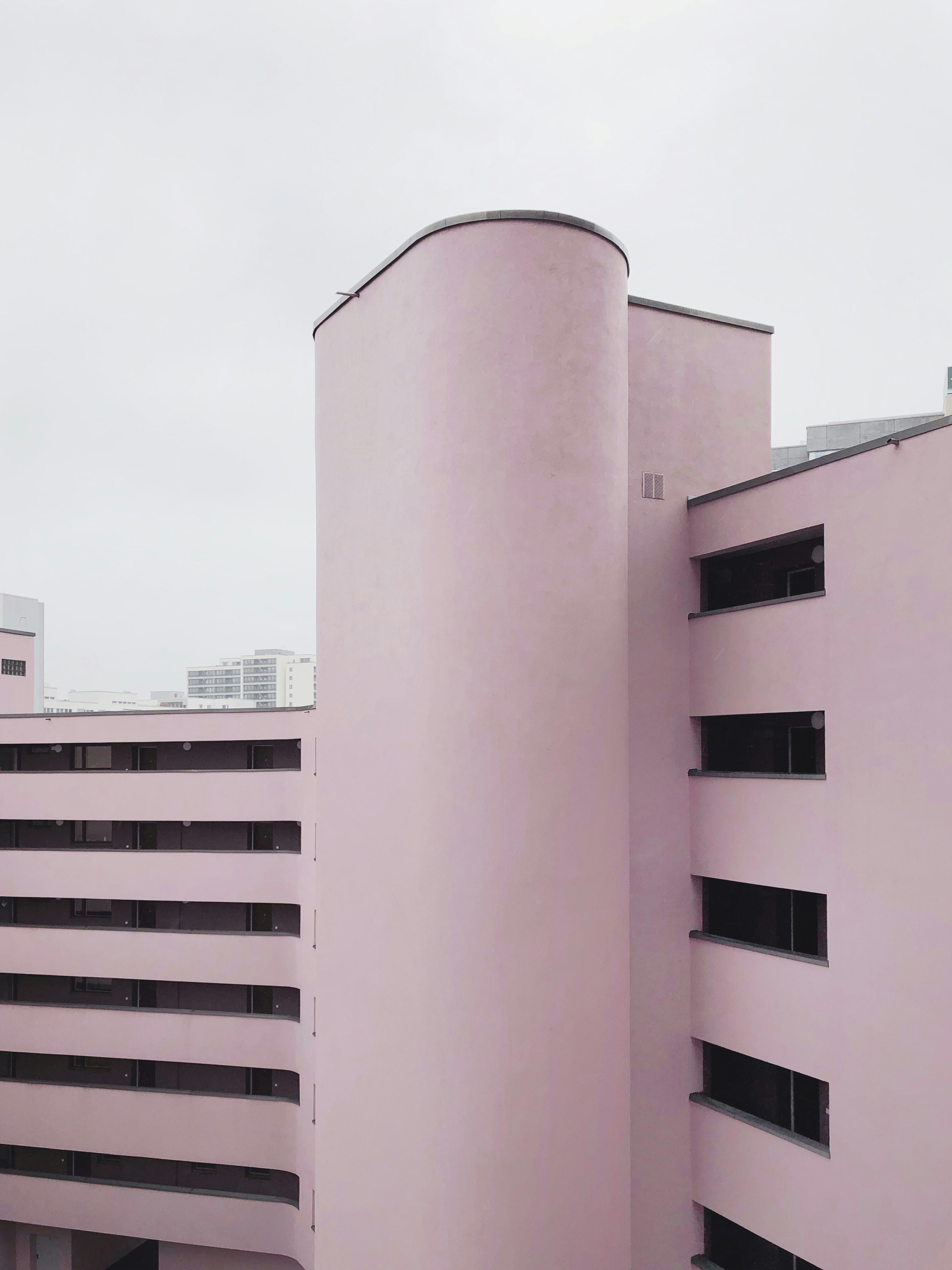 Architectural structure featuring smooth curves and soft pink tones against a cloudy sky. A minimalist design that evokes a sense of calm.