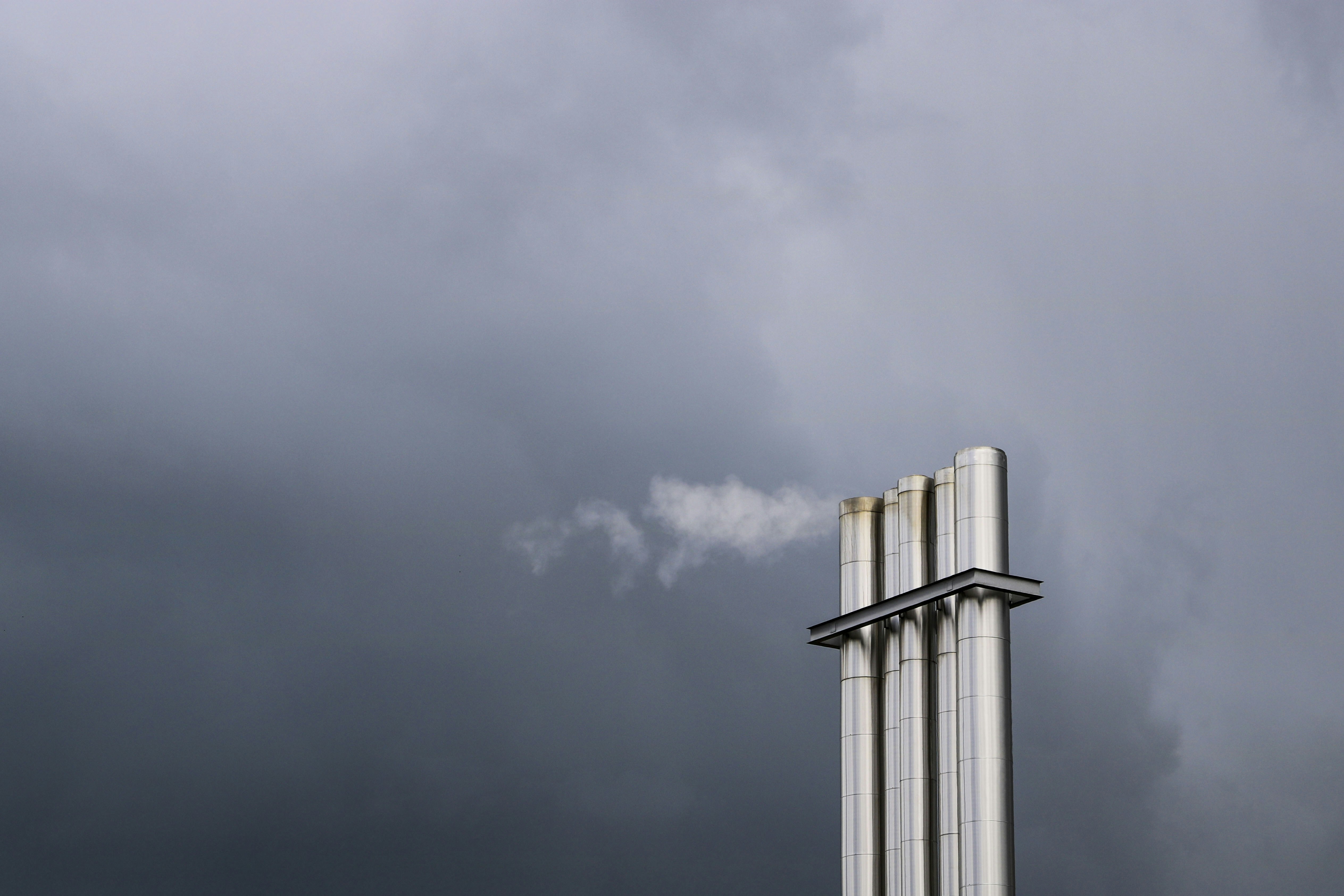 Industrial smokestacks releasing vapor against a backdrop of dark, ominous clouds.