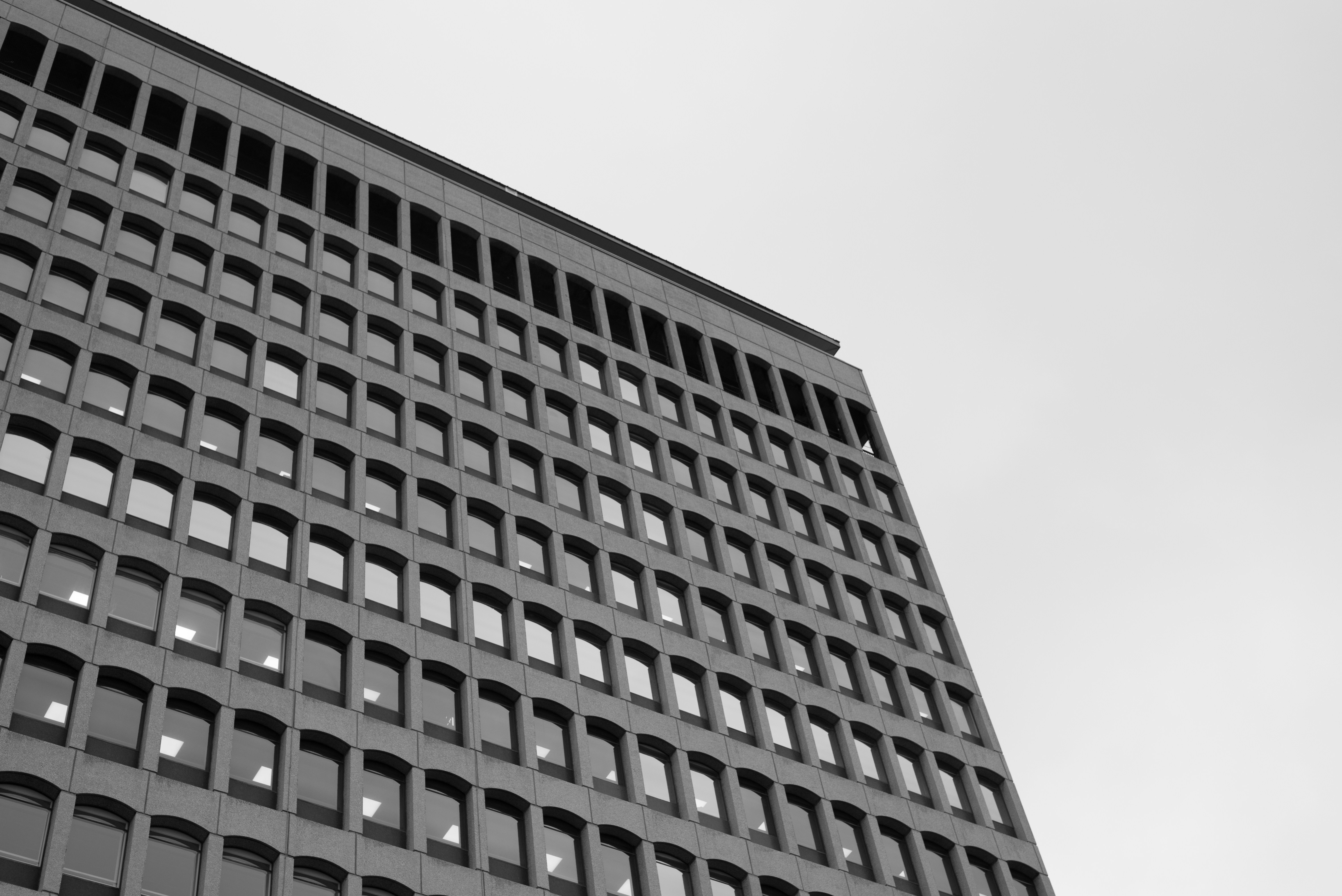 Black and white photo of a skyscraper's grid-like facade against a cloudy sky.