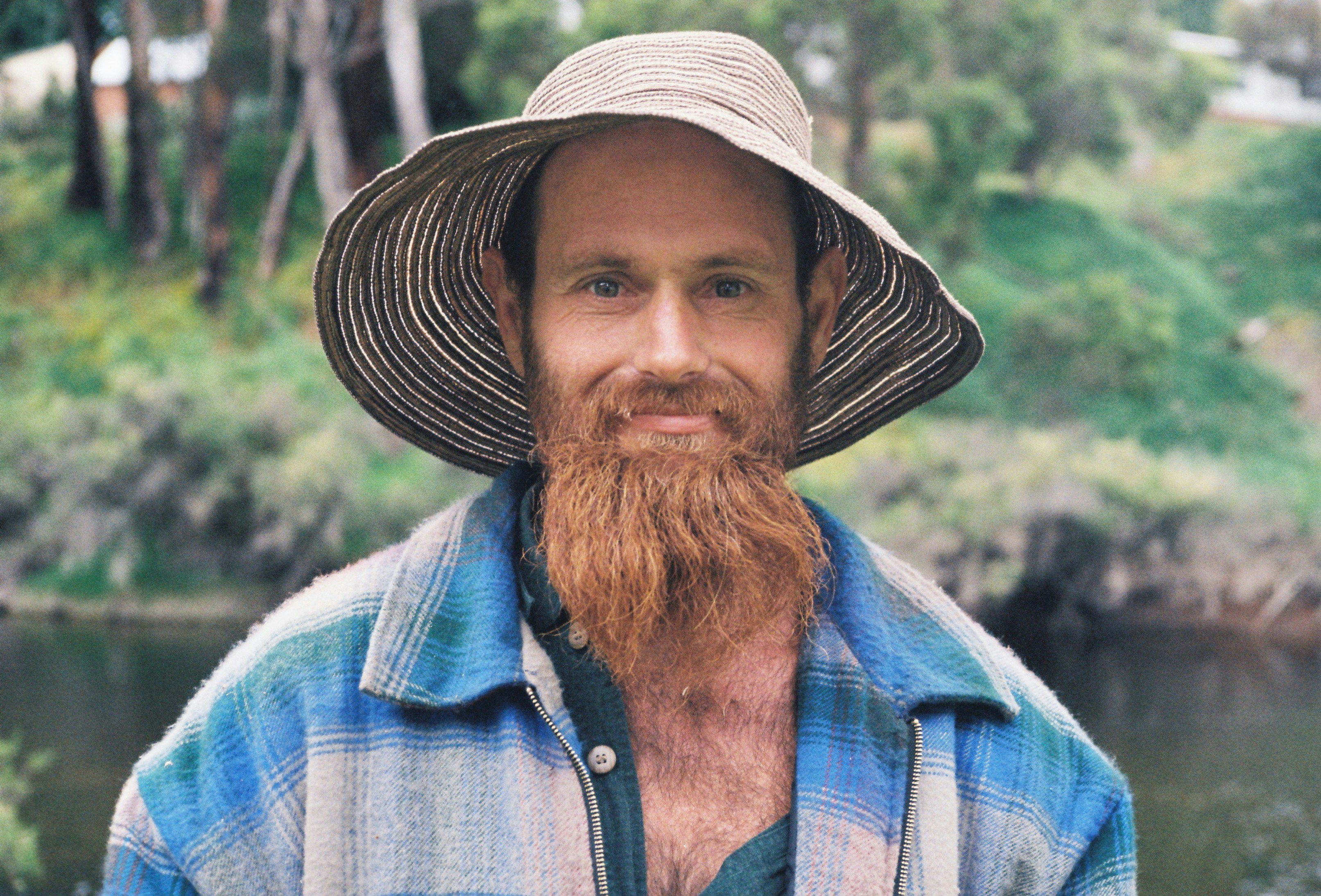 Riverbank Portrait: Rugged Bearded Wanderer in a Straw Hat