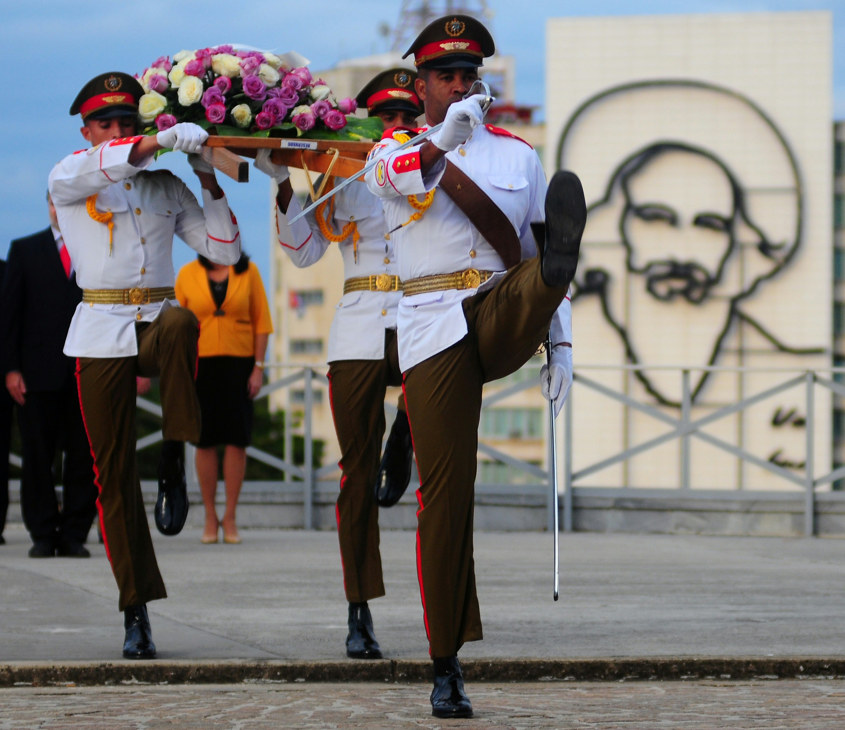 Stride of Honor: Uniformed Guards Carry a Floral Coffin Before a Monumental Relief