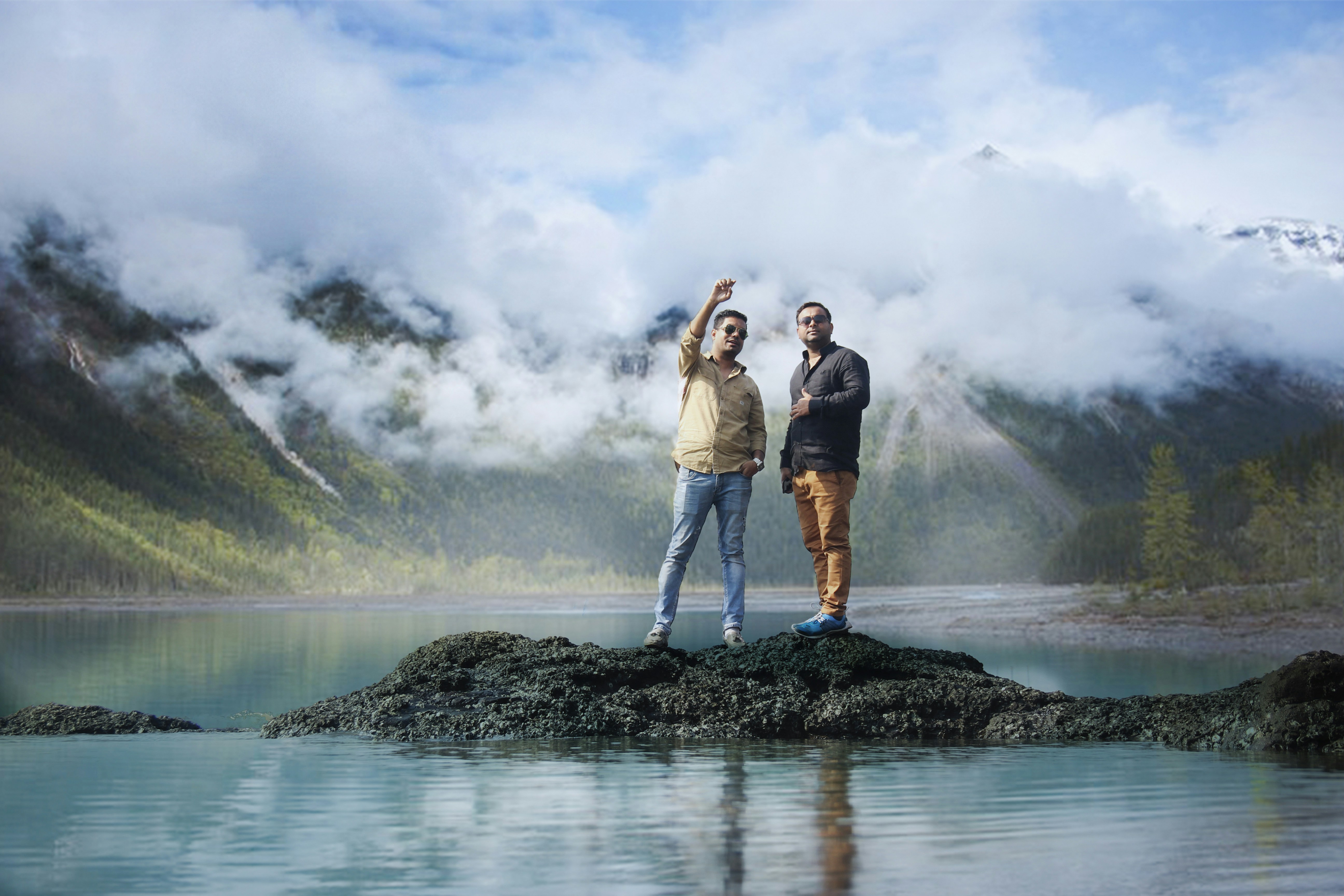 Two men standing on black rock surrounded by lake photo – Free Grey ...