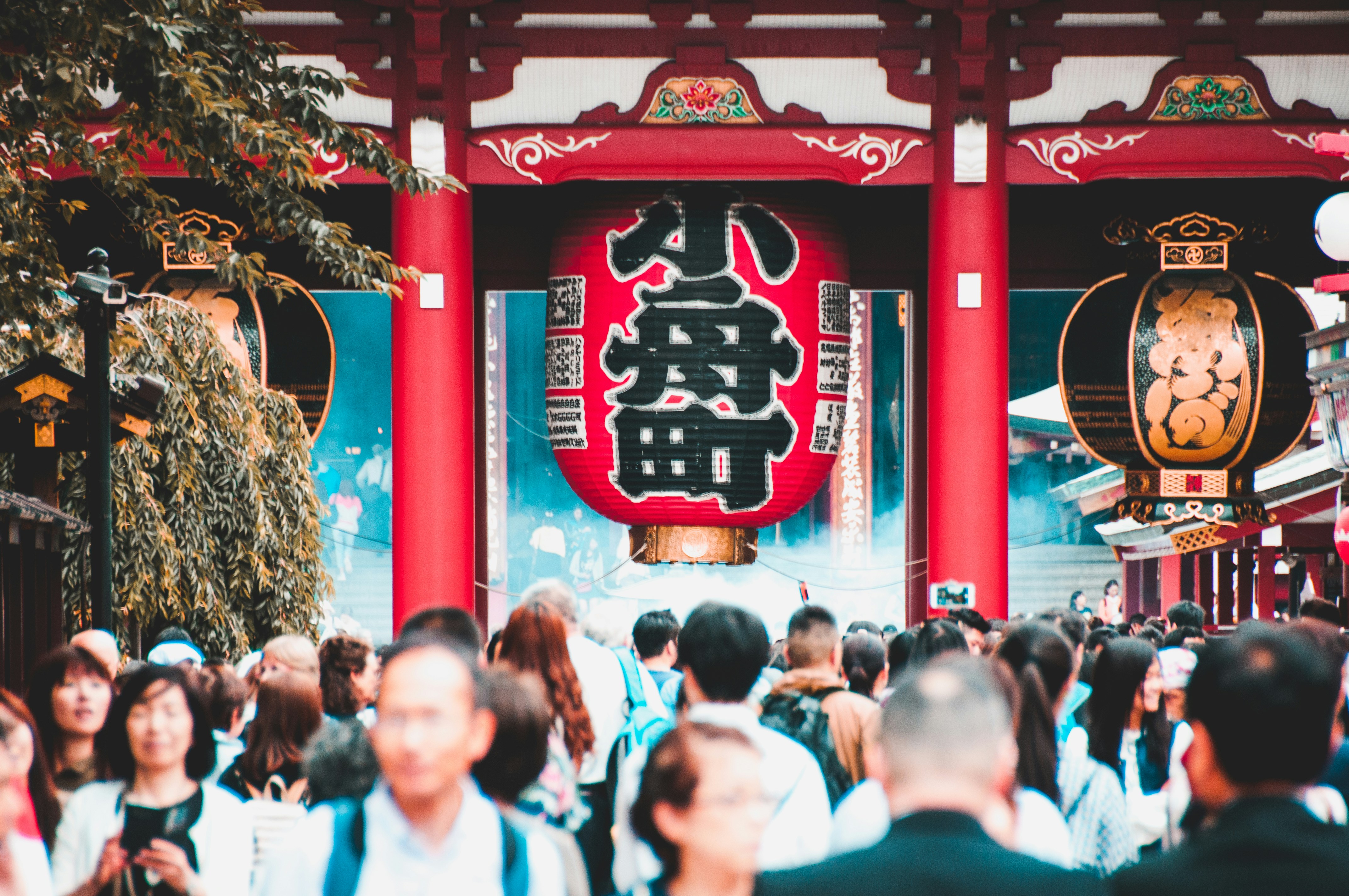Crowd of visitors navigating through a vibrant red temple gate adorned with a large lantern, showcasing a blend of culture and community.