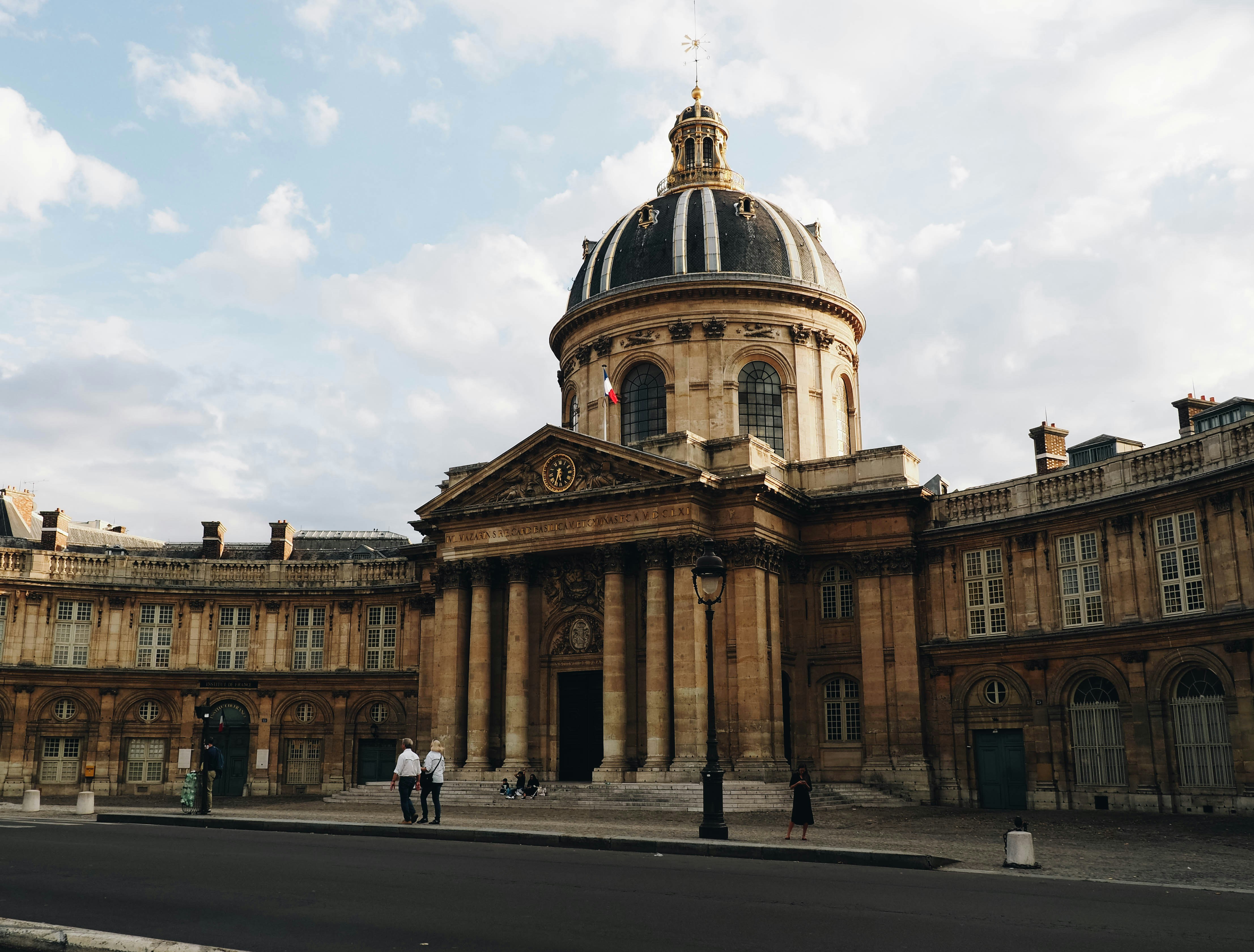 Historic building featuring a grand dome and classical architecture, set against a dramatic sky. The scene captures the essence of Parisian culture and history.