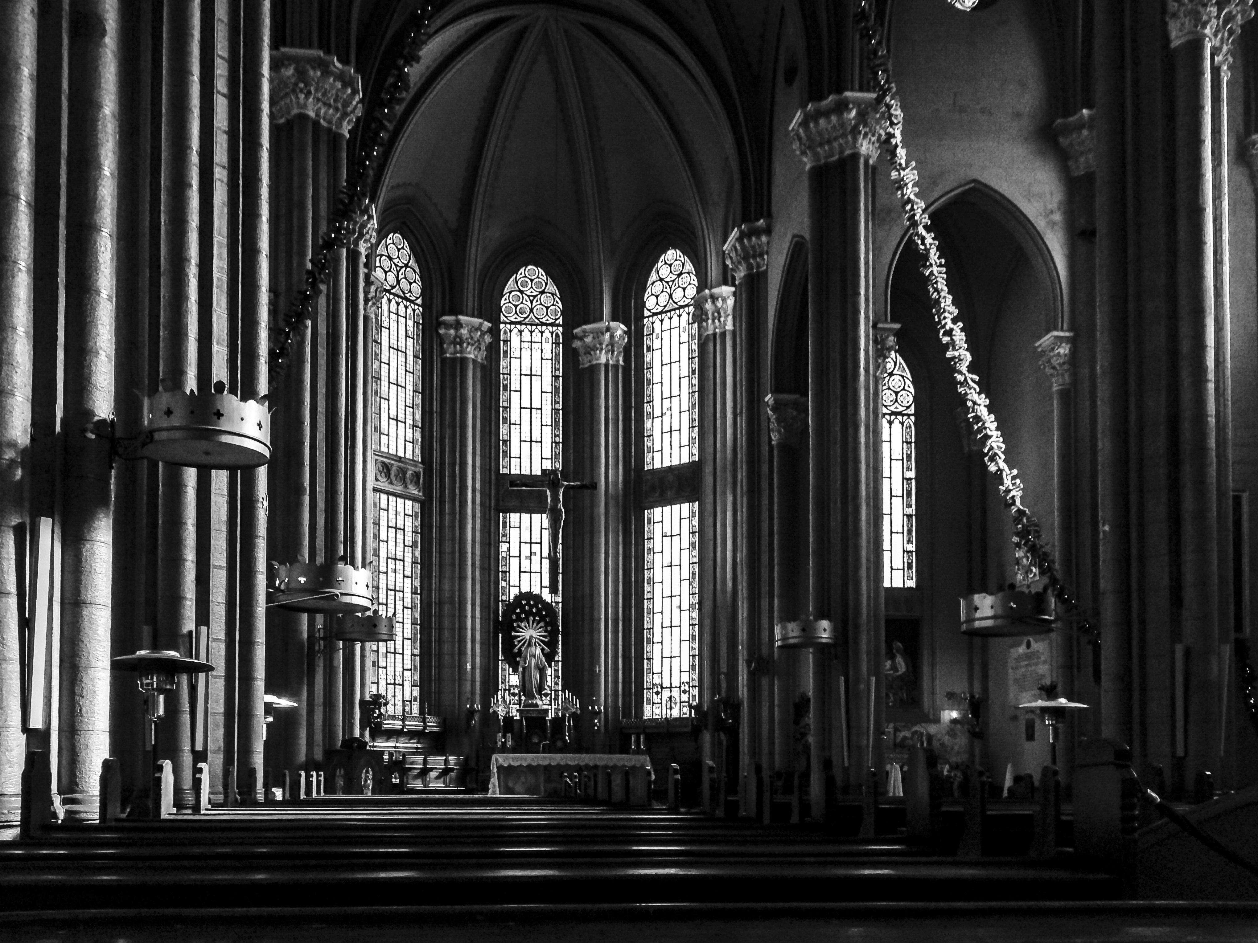 Sunlight streams through ornate stained glass windows of a Neo-Gothic church interior.