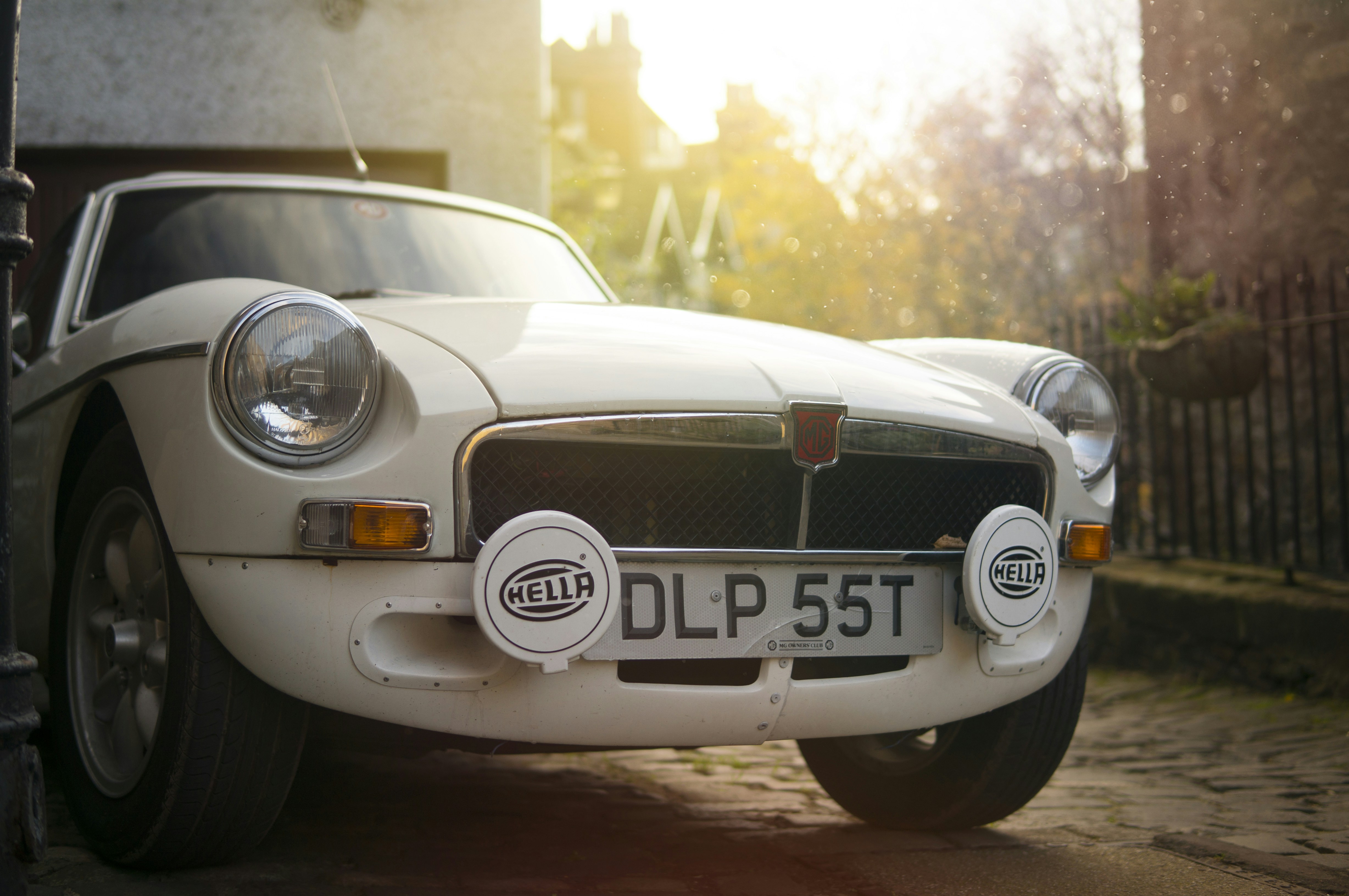 Vintage white car with prominent headlights parked on a cobblestone street, bathed in warm sunlight.