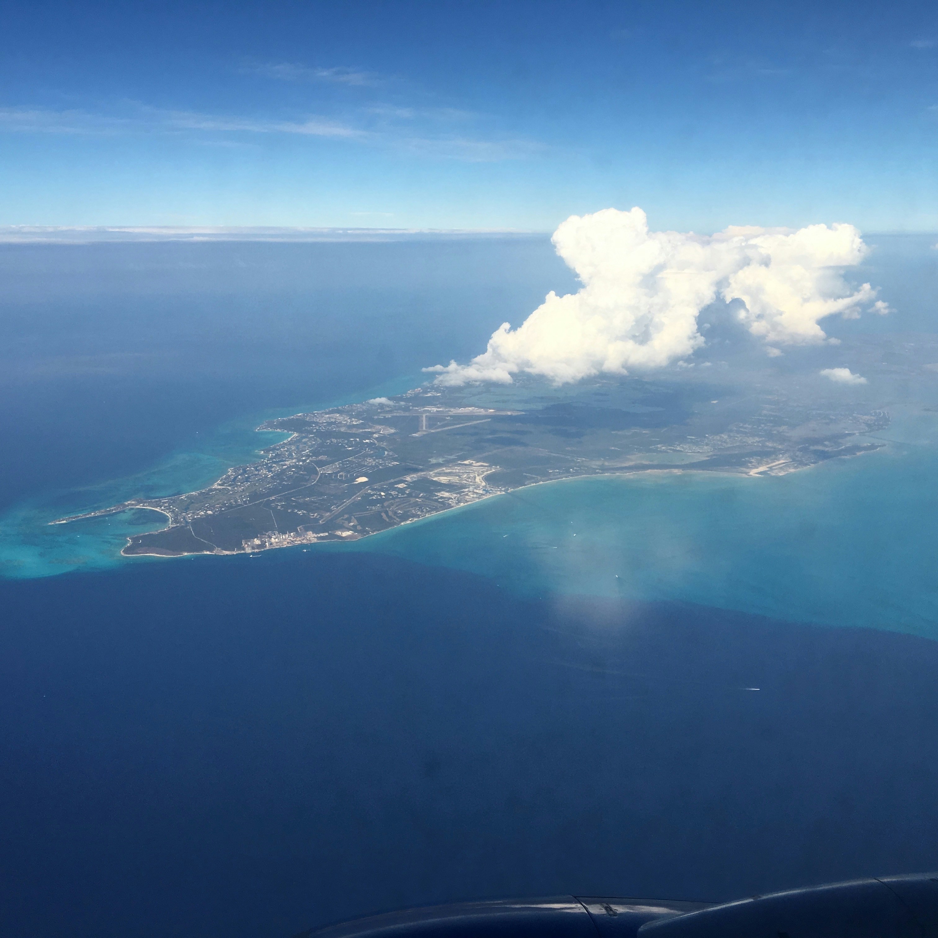 Aerial view of a green island surrounded by turquoise waters and fluffy clouds.
