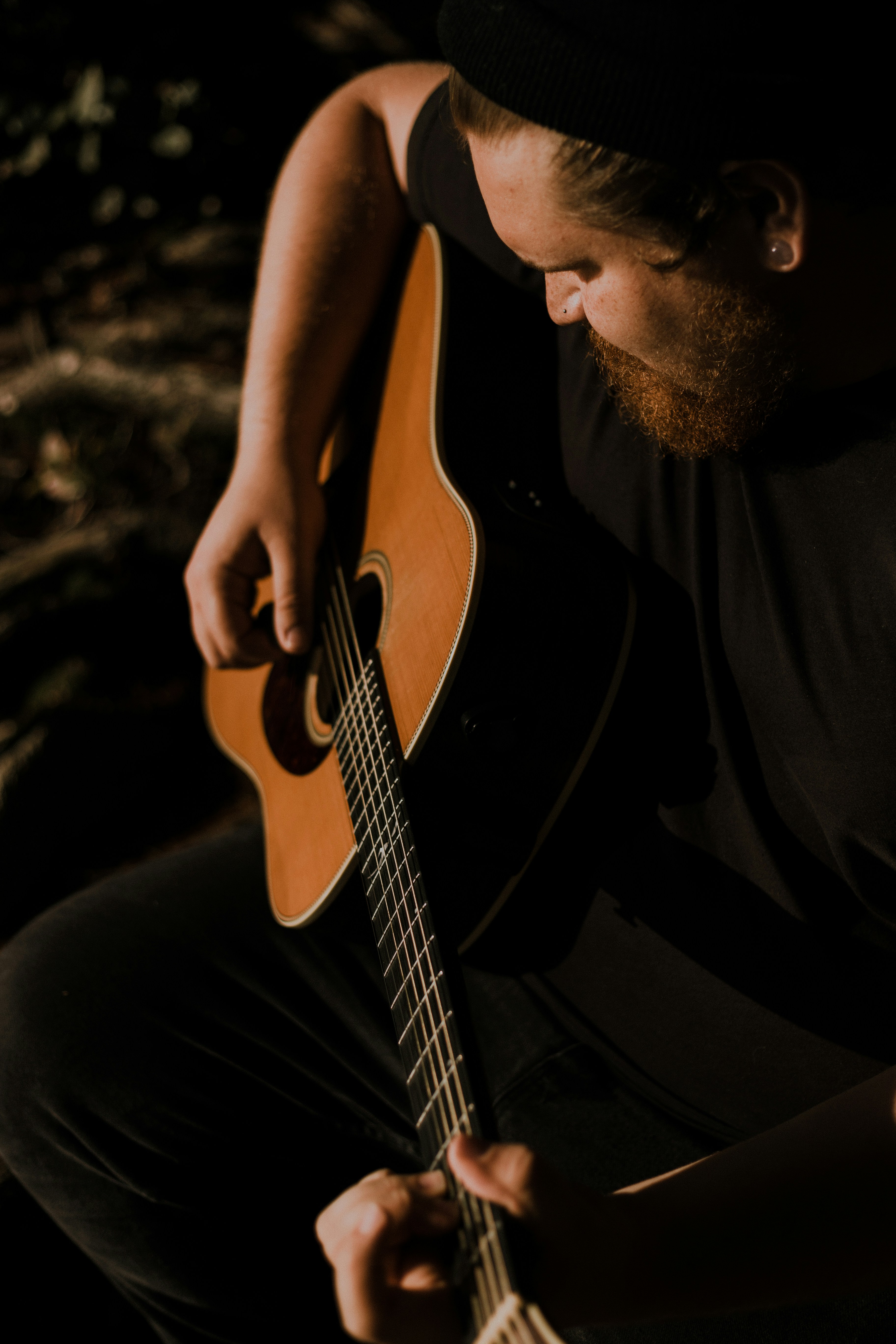 Musician strumming an acoustic guitar, immersed in a sunlit forest setting. The focus is on the intricate details of the guitar and the musician's expression.