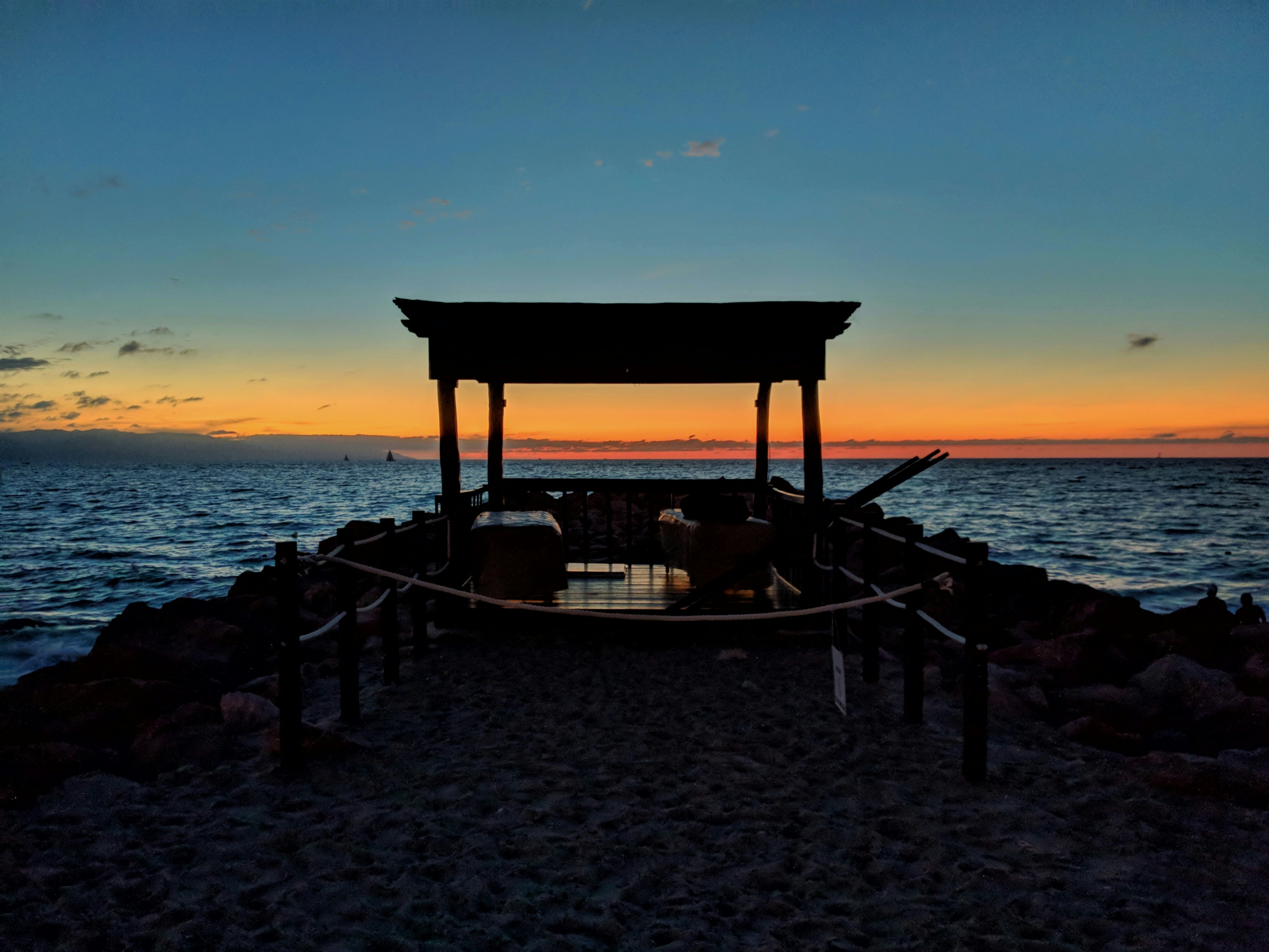 Silhouetted pavilion overlooking a tranquil ocean at sunset.