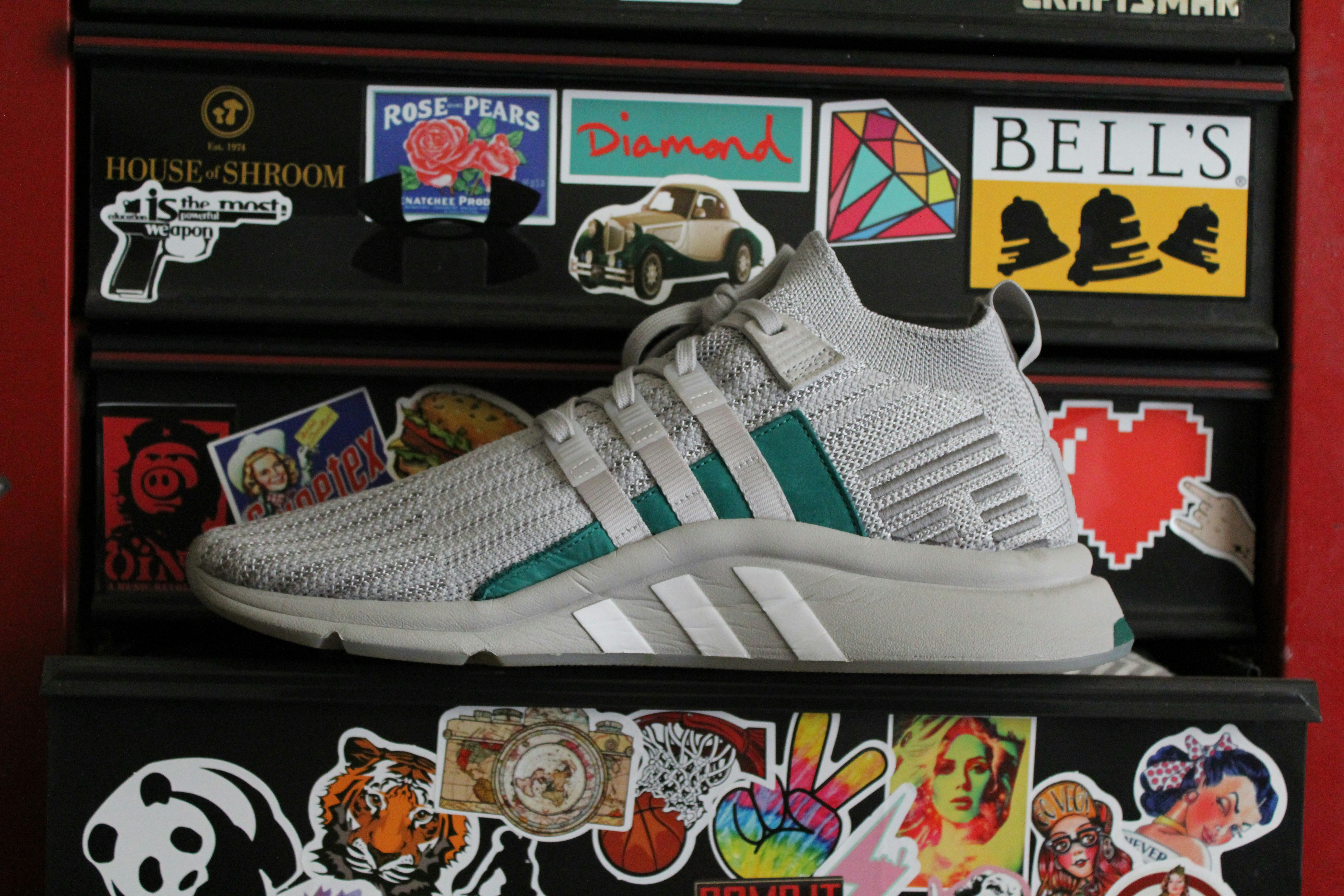Sticker-Backed Sneaker Spotlight: A Teal-Trim Glide on a Wall of Decals