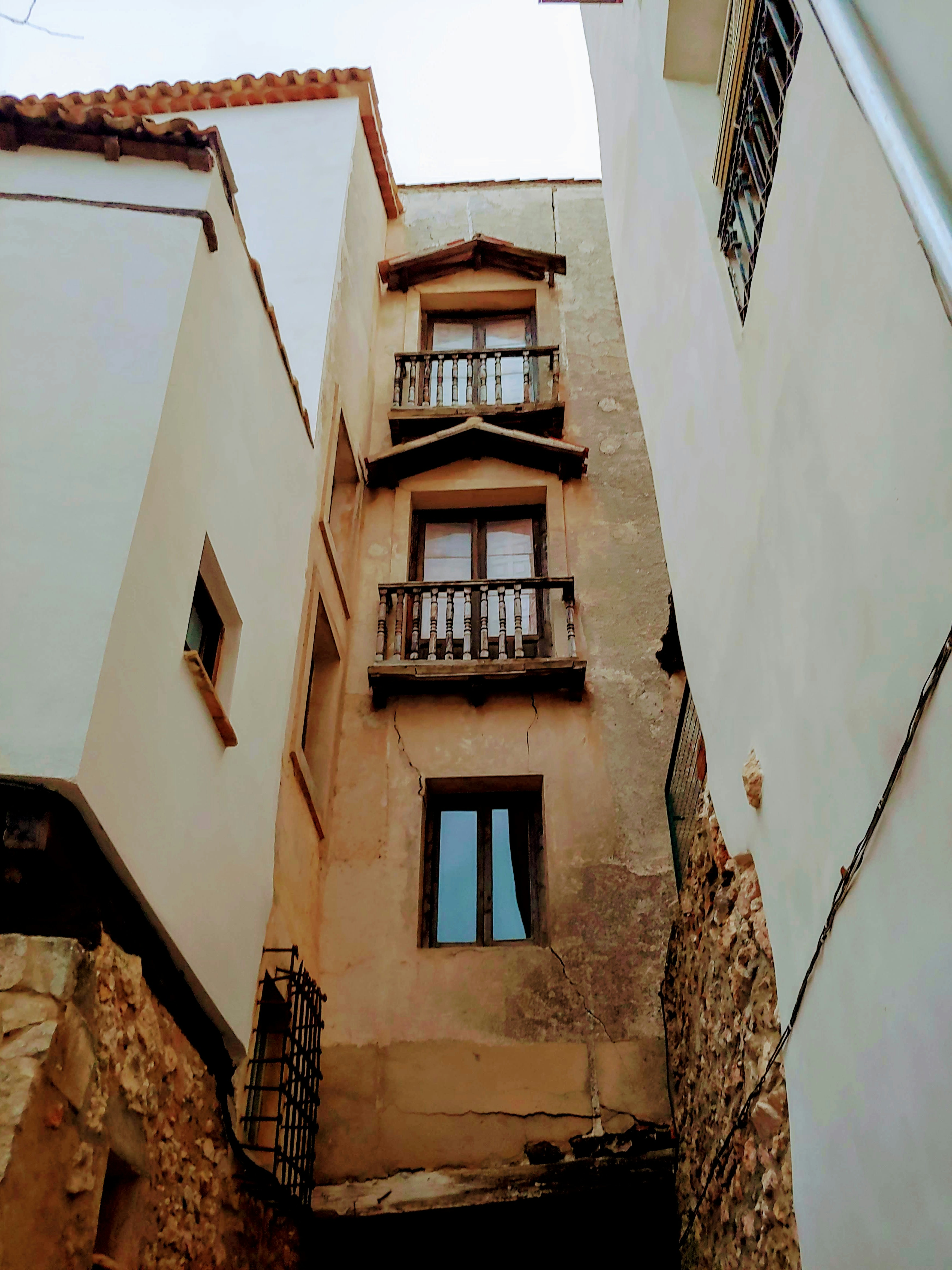Narrow alleyway showcasing a vintage building with wooden balconies nestled between two white structures.