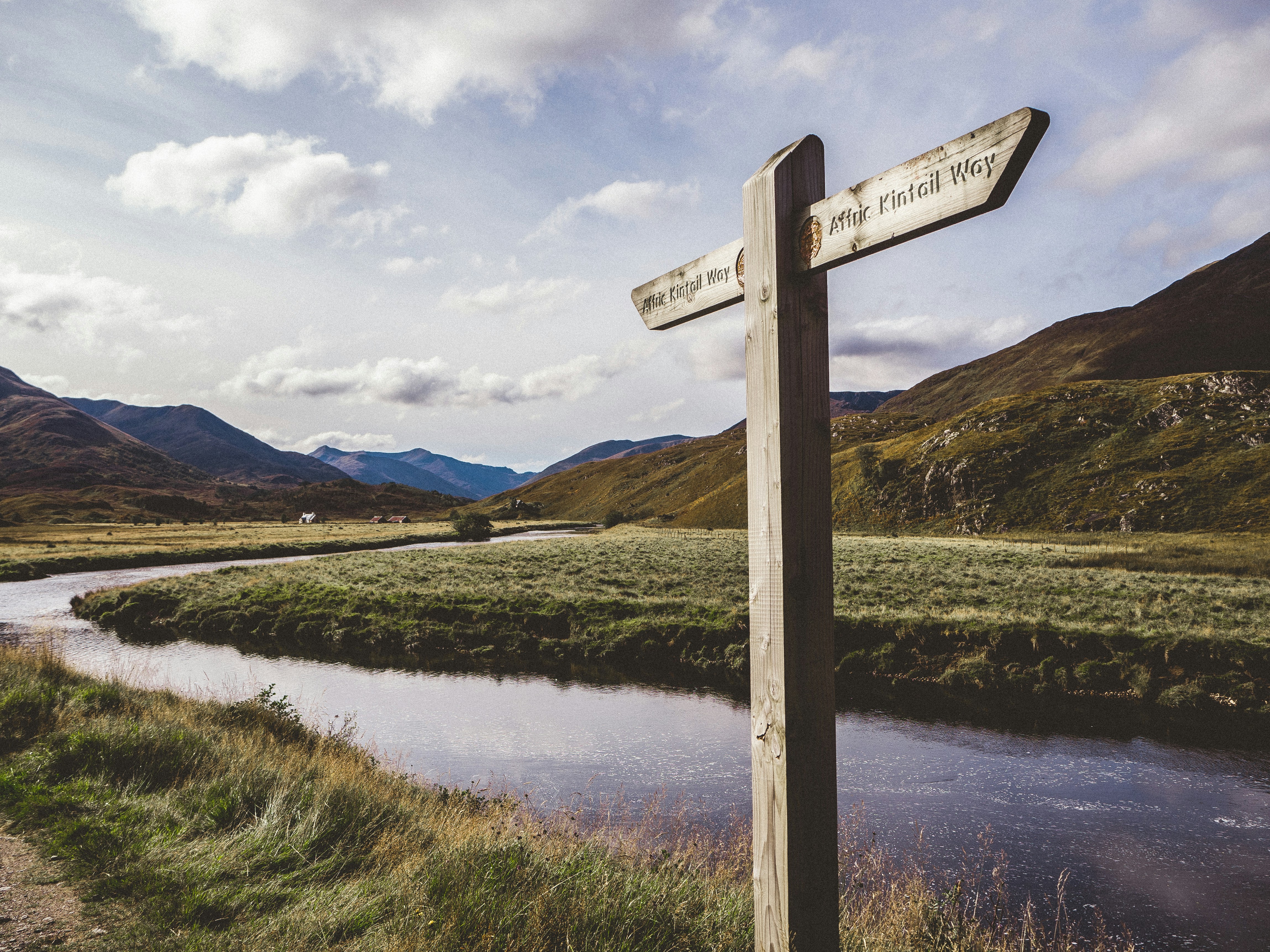Wooden signpost directing travelers along the scenic route beside a winding river in the Scottish Highlands.