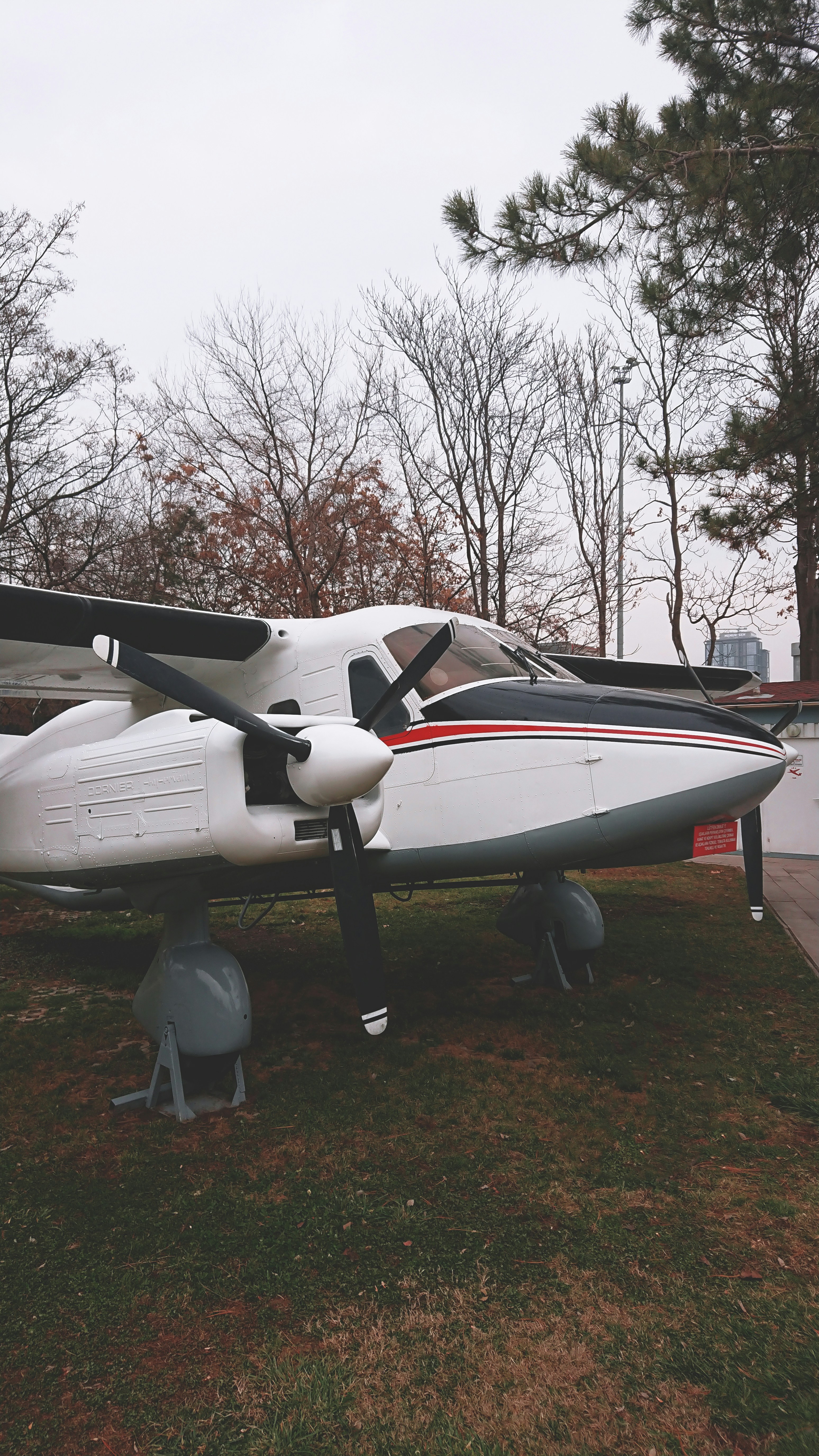 White twin-prop aircraft on display under leafless trees