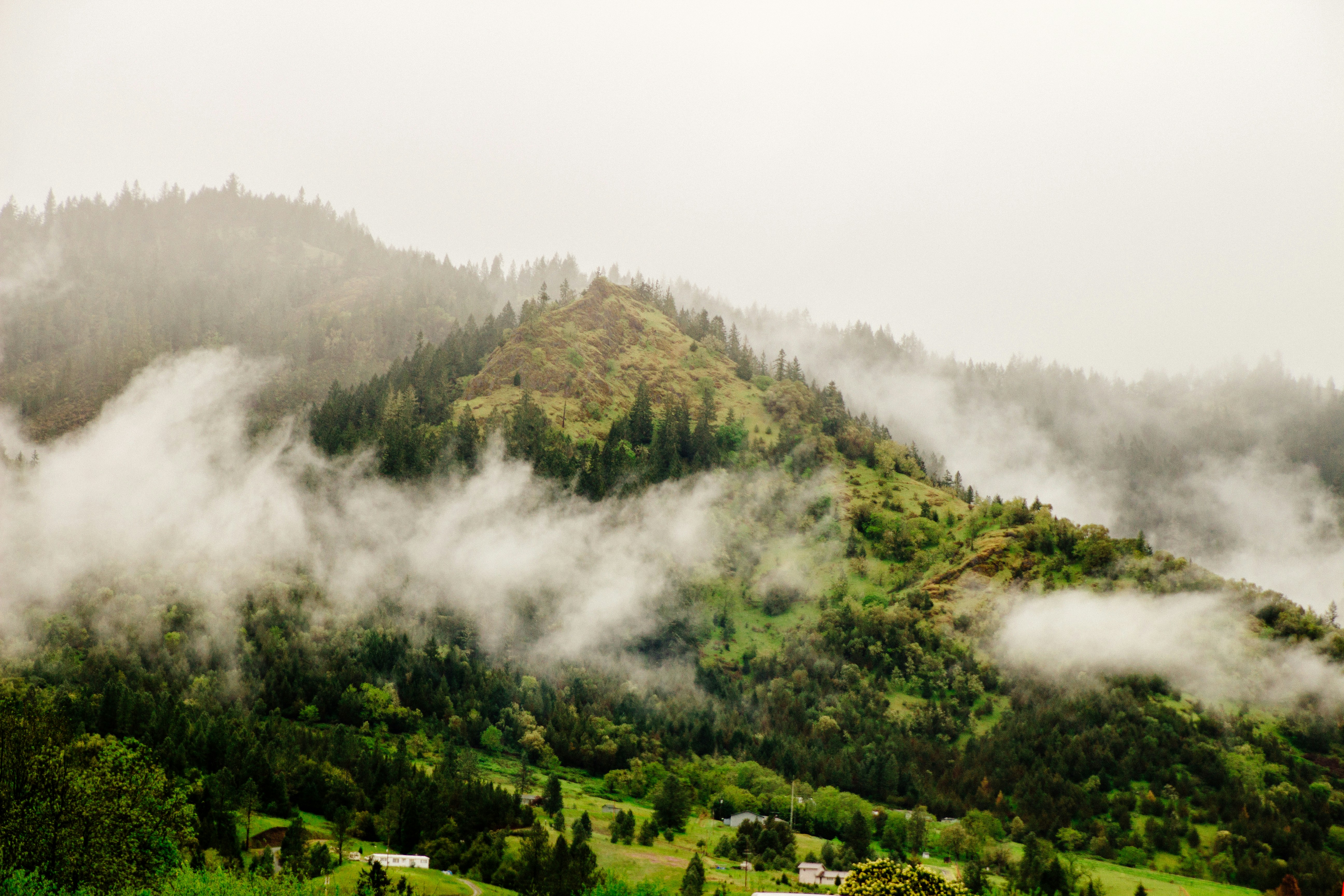 Lush green mountains shrouded in mist, with a hint of sunlight breaking through the clouds. The serene landscape captures the essence of nature's tranquility.