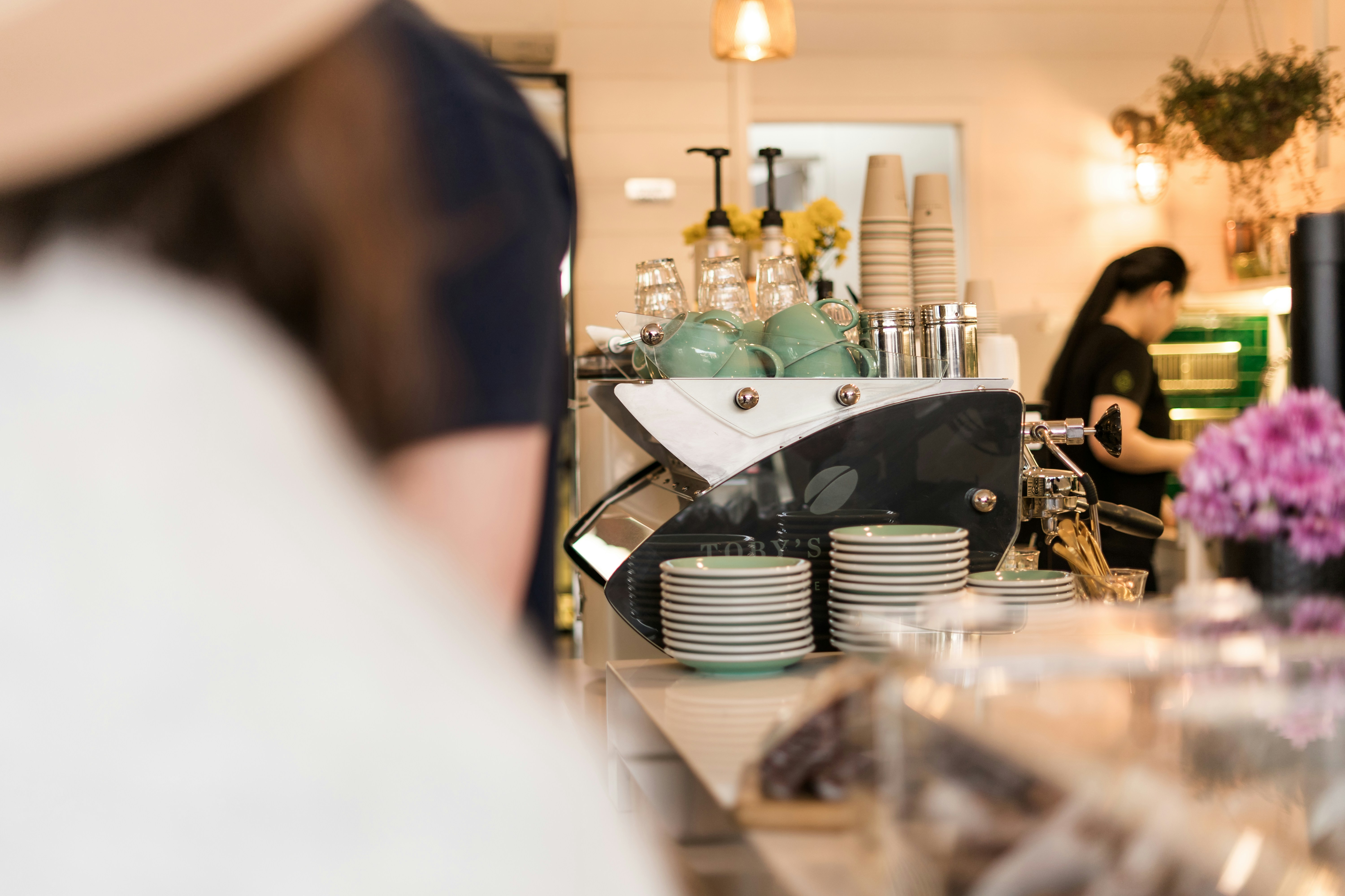 Barista preparing drinks at a modern café, with stacked cups and a coffee machine in the foreground.