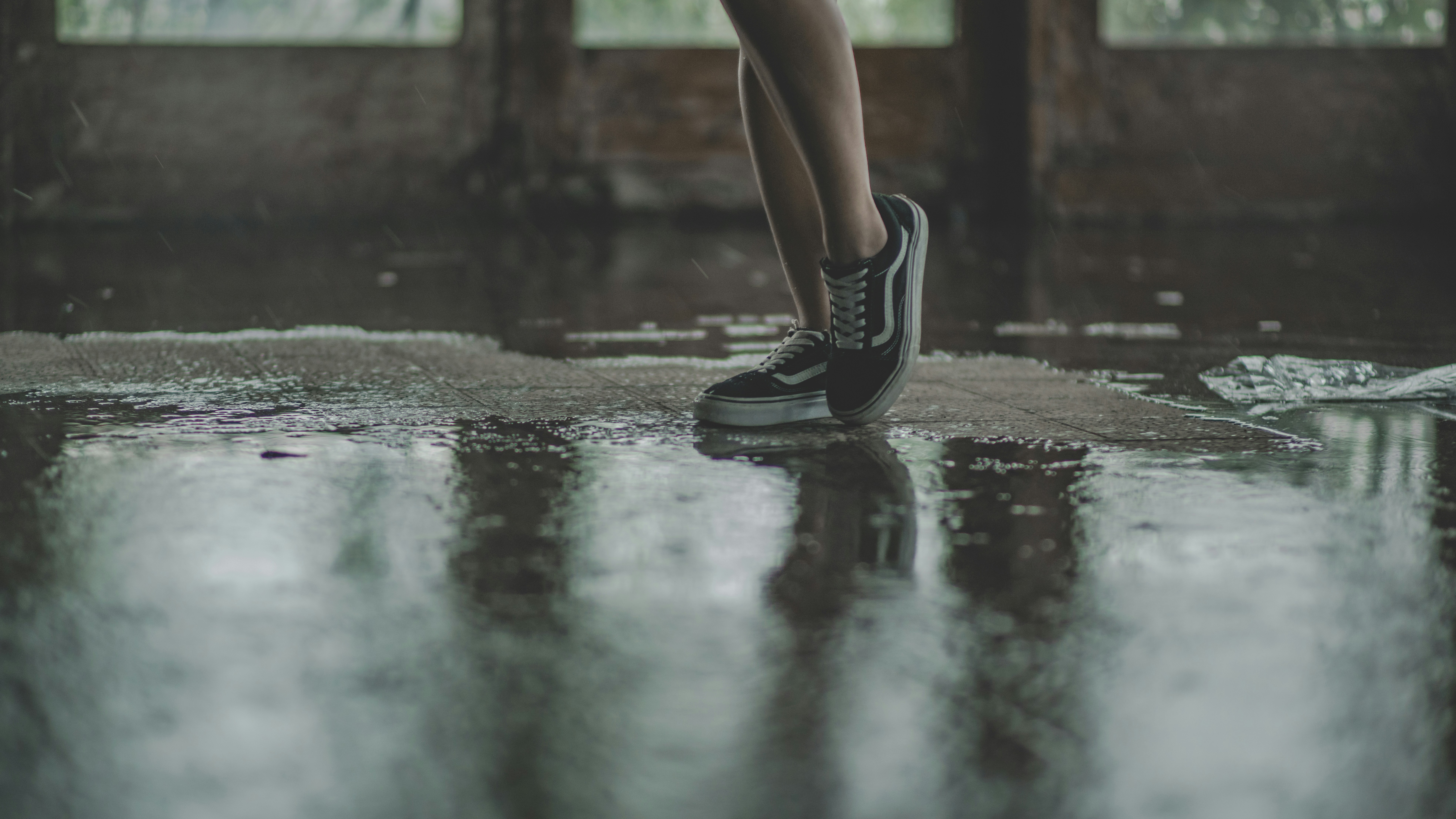 A lone figure stands on a wet surface, showcasing stylish black and white sneakers amidst a serene, reflective environment.