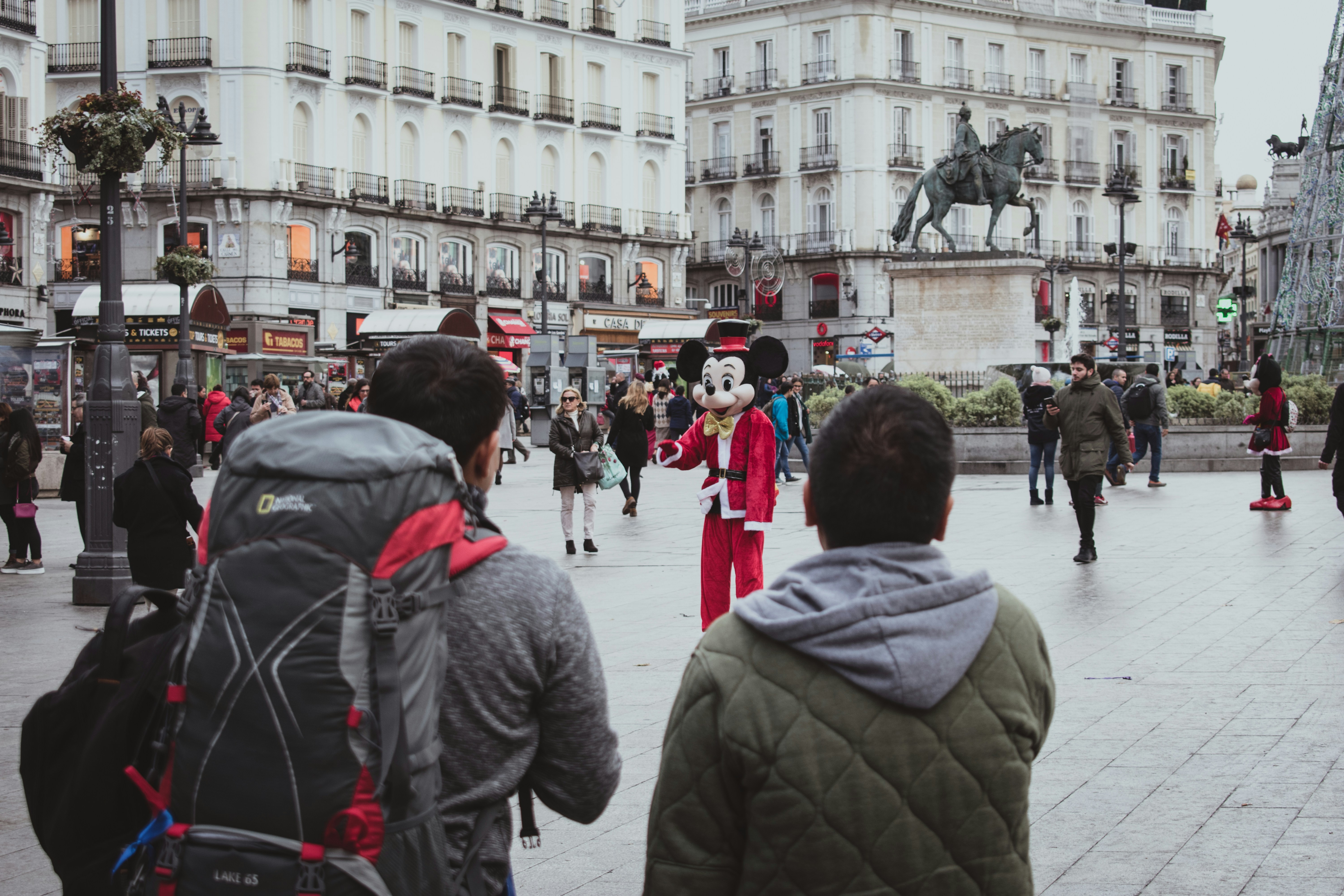 A costumed character entertains passersby in a bustling urban square, surrounded by historical architecture and curious onlookers.
