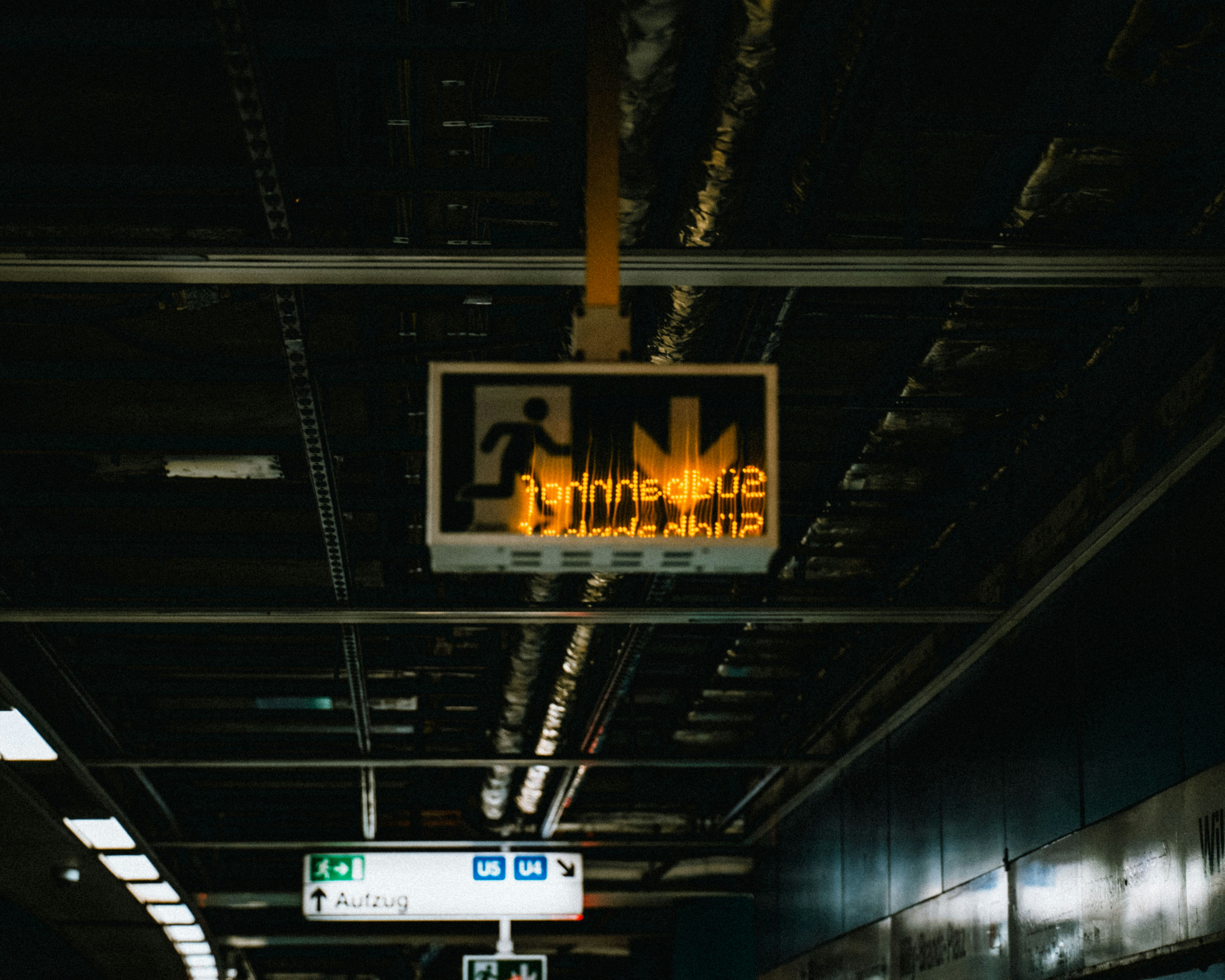 Illuminated directional sign indicating the way to a subway exit in a dimly lit underground station.