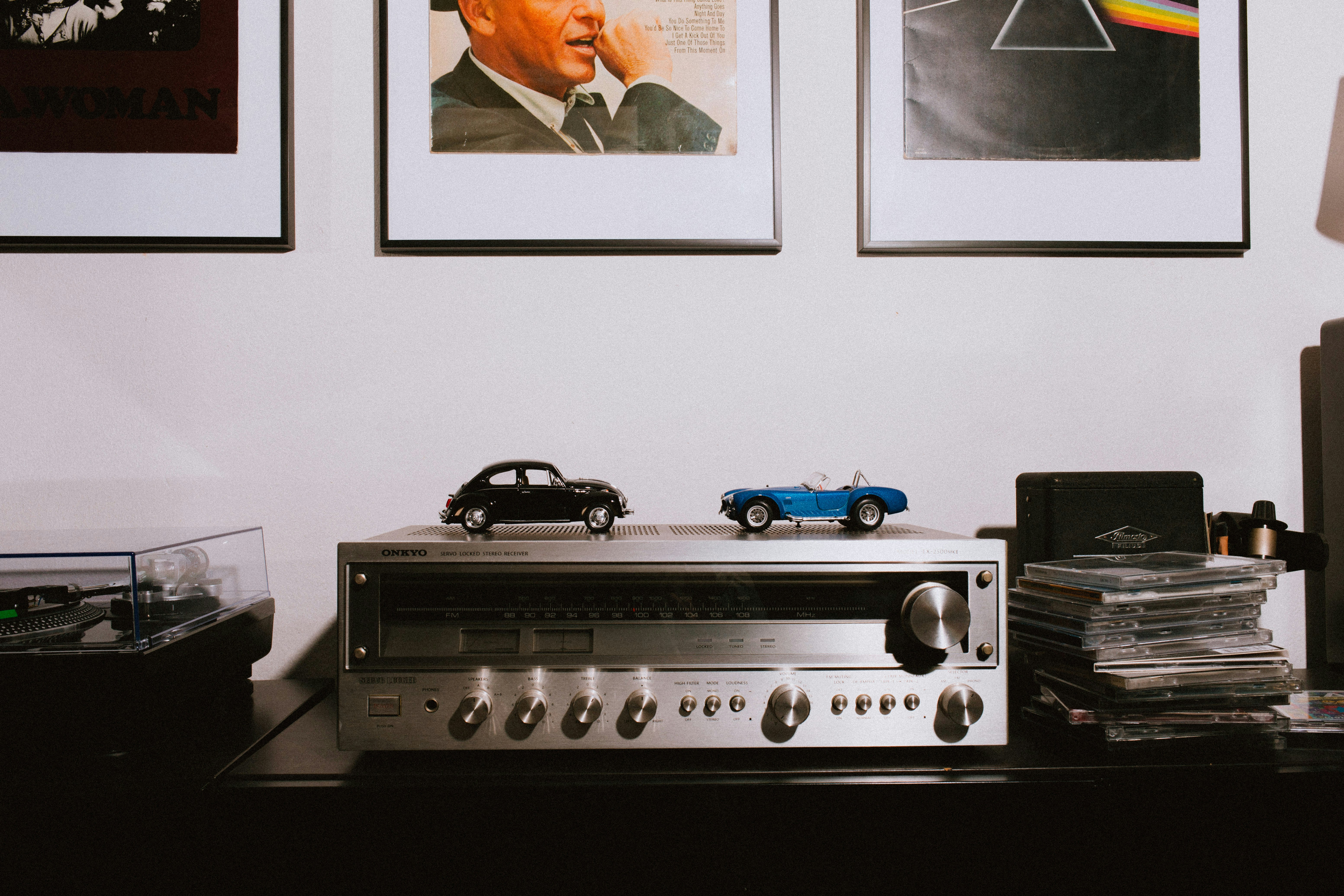 Classic stereo receiver adorned with miniature car models, surrounded by vinyl records and framed art. A blend of music and nostalgia.