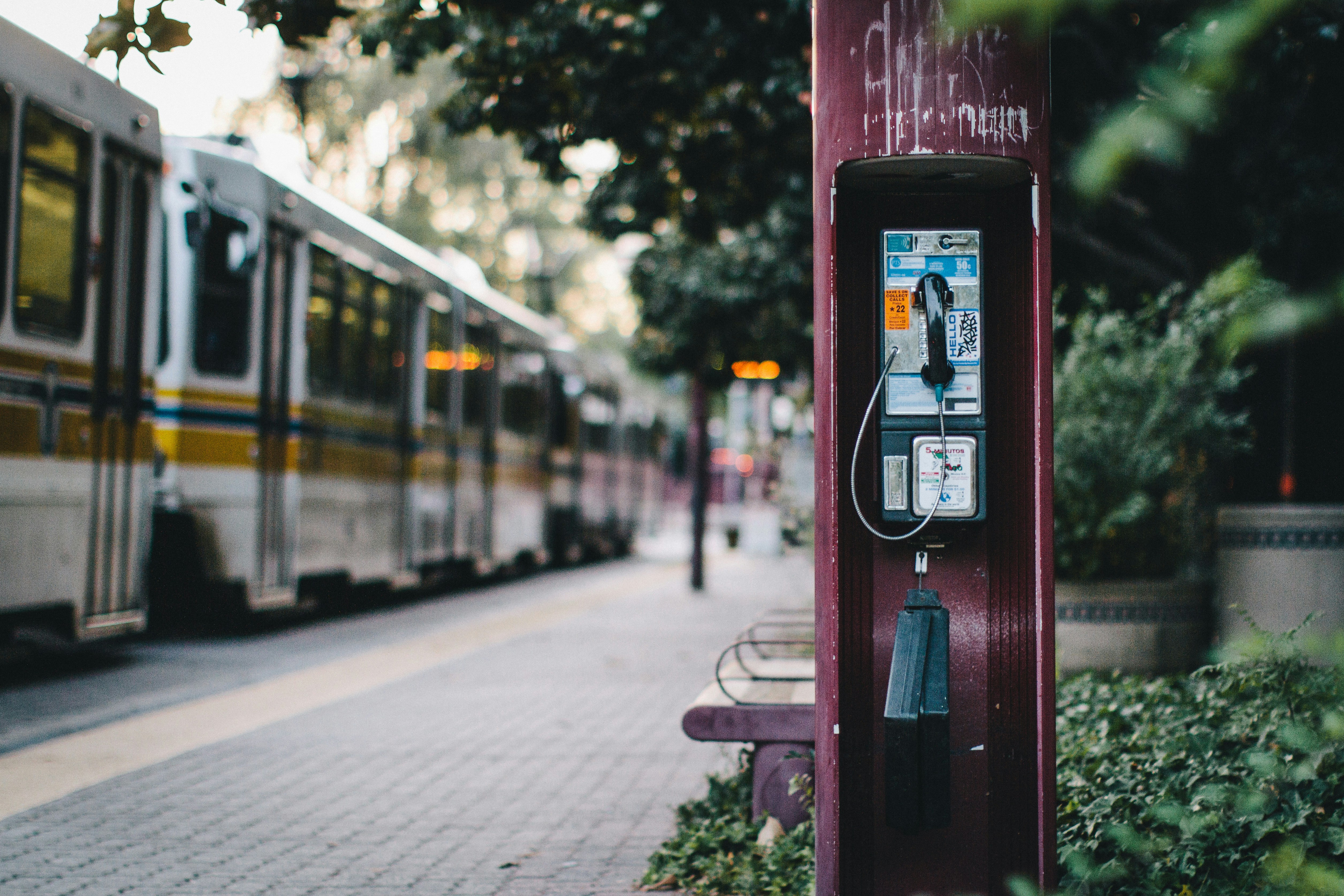 Vintage payphone stands beside a stationary train under leafy trees.