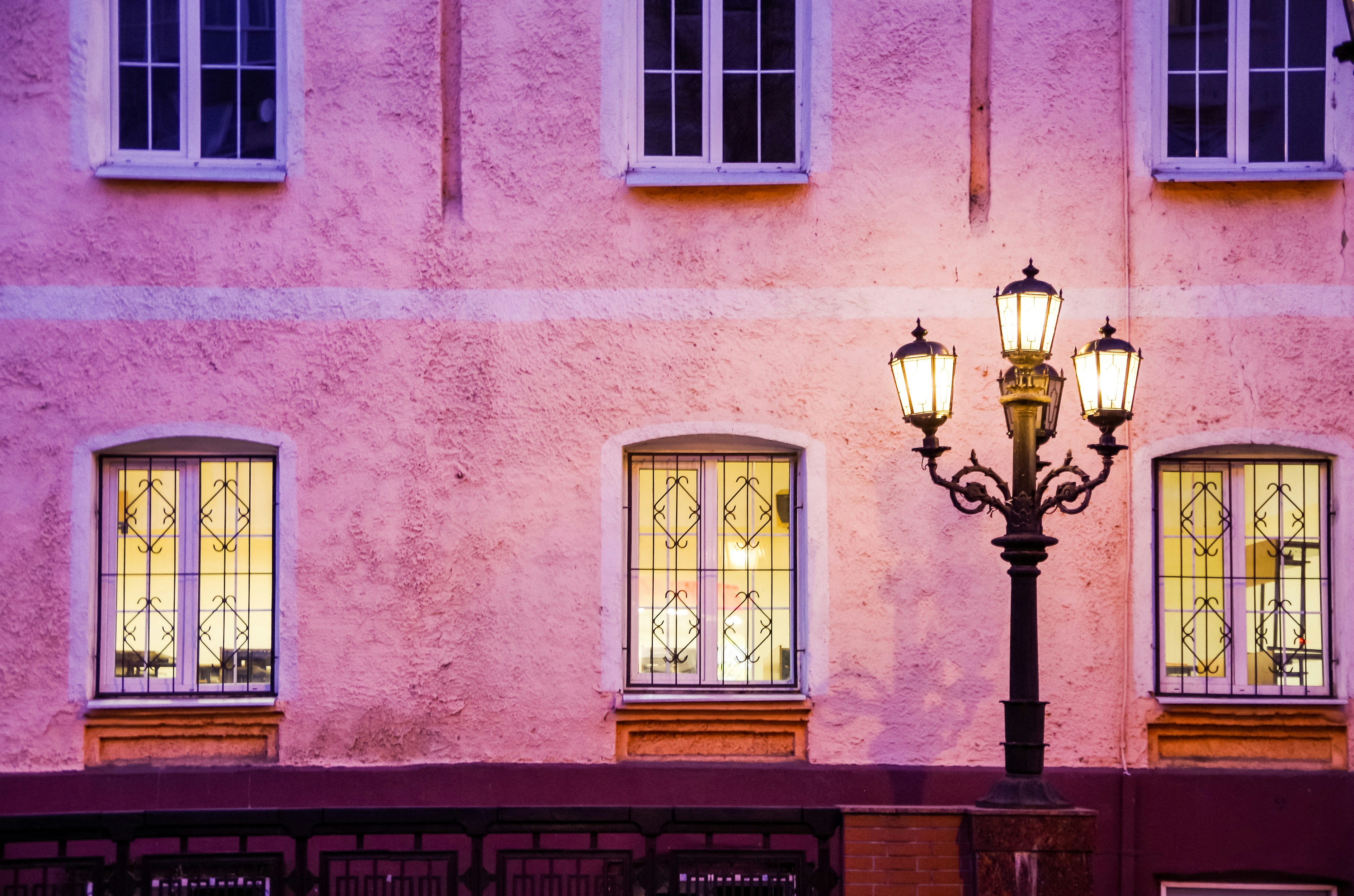 Streetlamp casting warm light against a pink-hued building with illuminated windows at dusk.