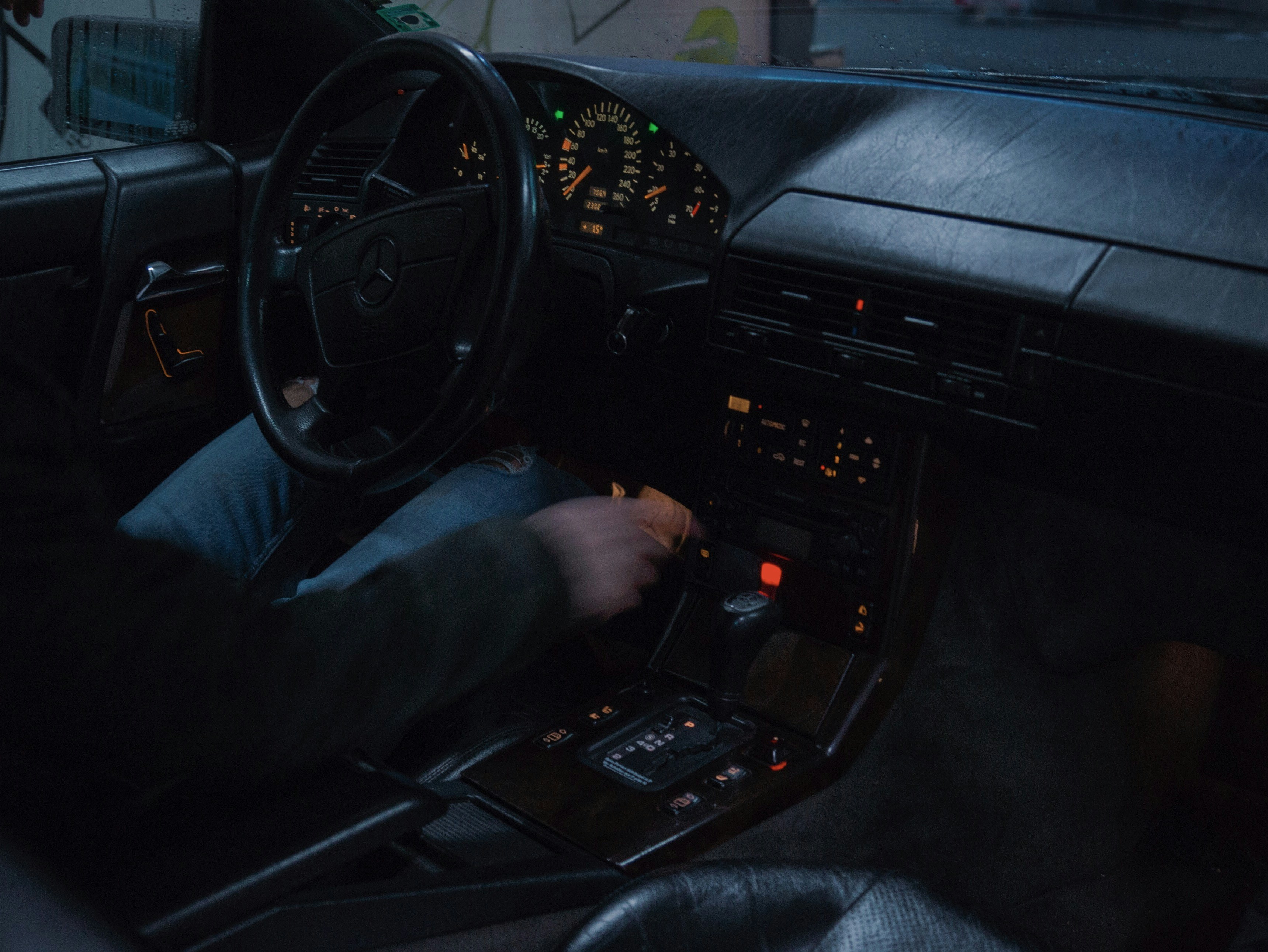 Driver adjusting controls on a vintage car's dashboard during nighttime.