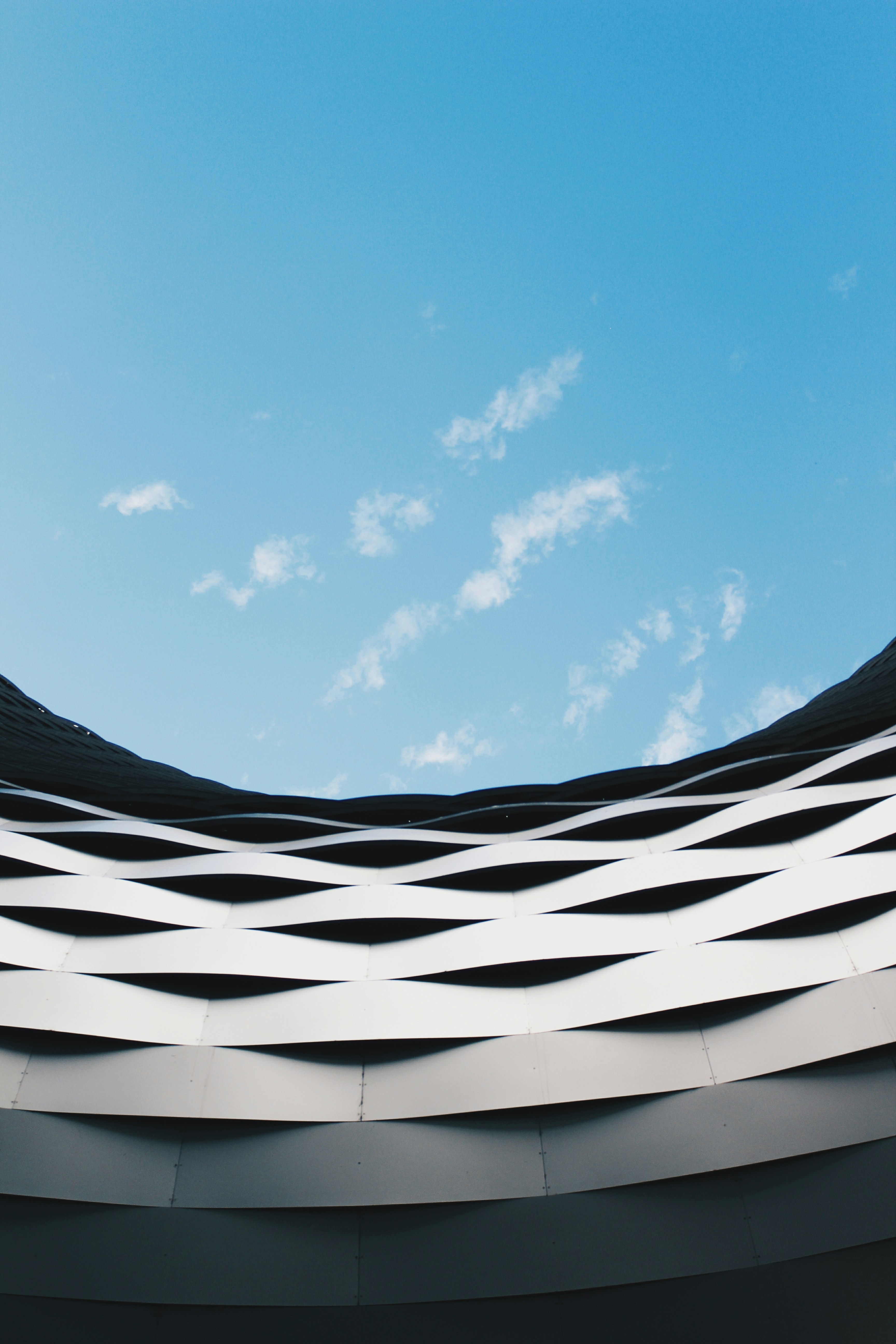 Dynamic architectural facade with flowing lines against a bright blue sky, showcasing modern design elements. 