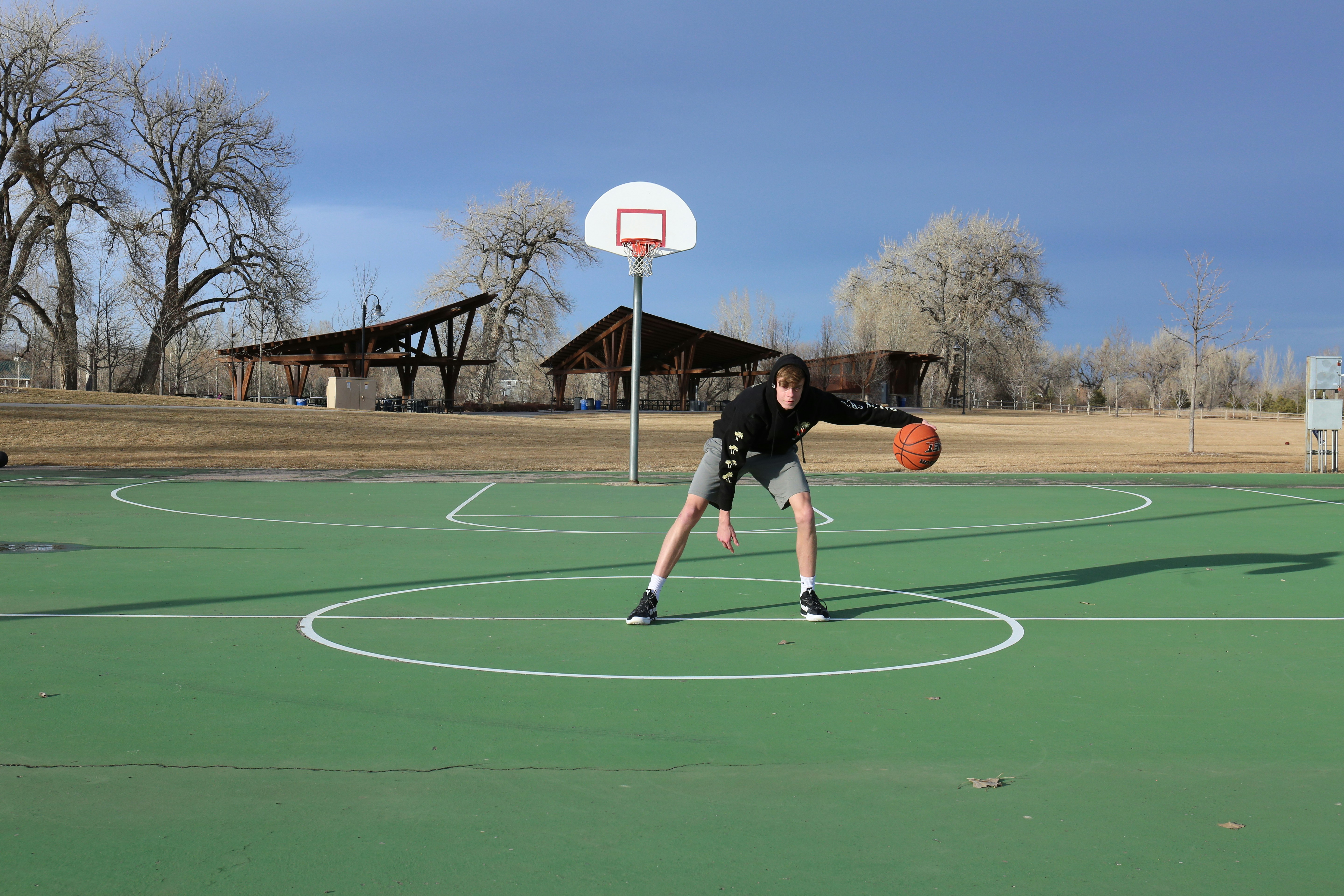 Young athlete performing a basketball dribble on an outdoor court with a dramatic sky in the background.