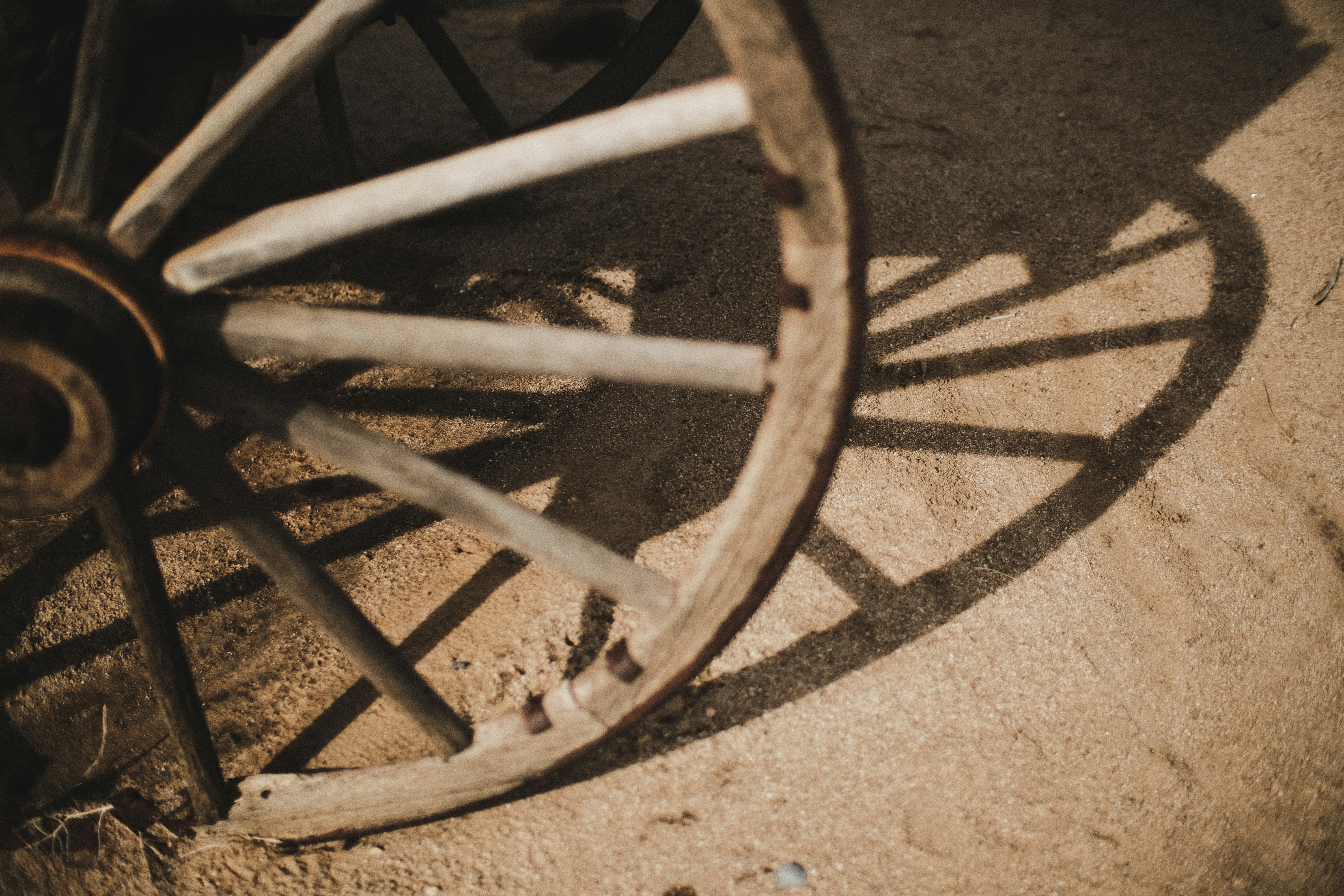 Weathered wooden wheel casting intricate shadows on sandy ground, showcasing the interplay of light and texture.