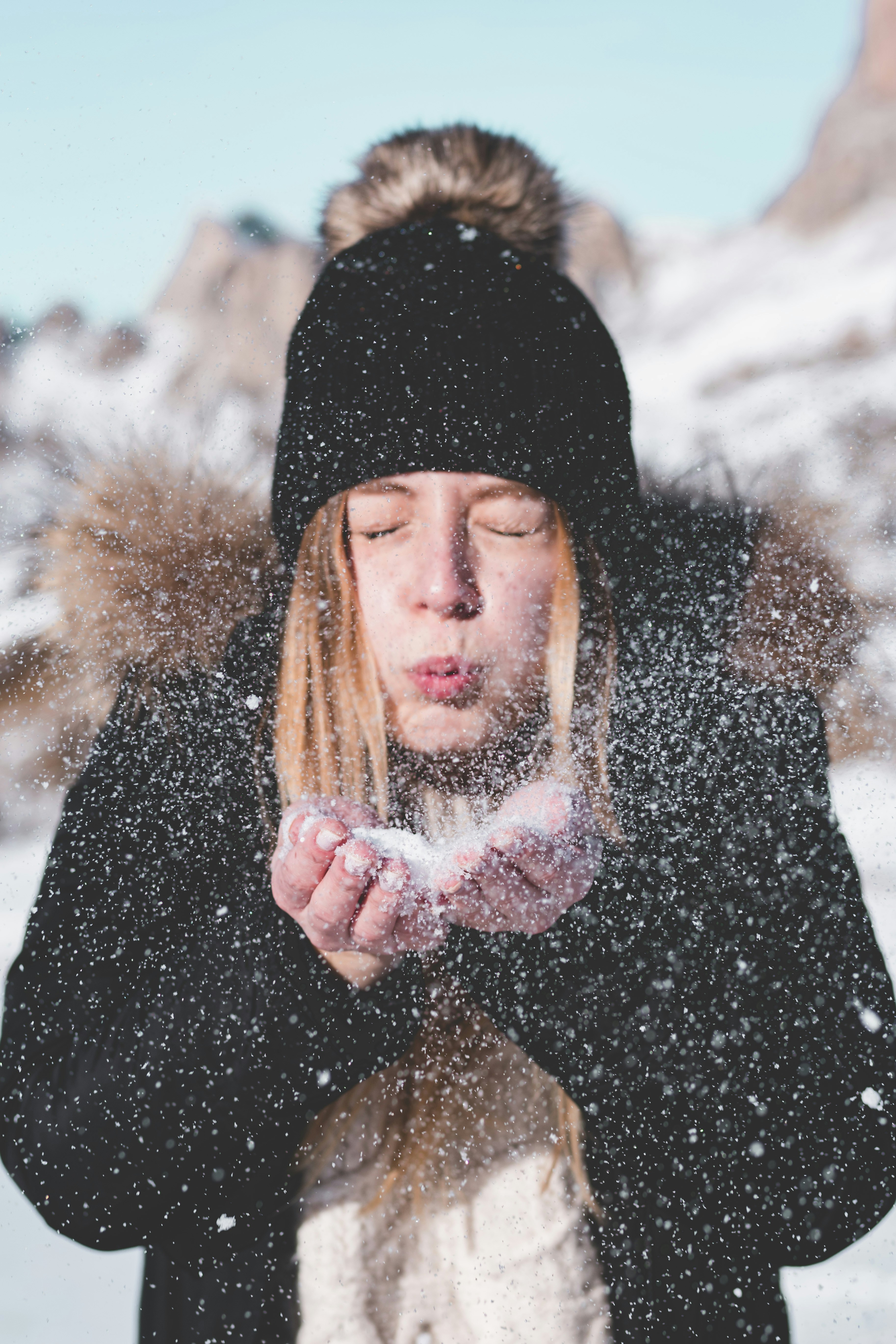 Woman wearing black bobble hat and hooded fur jacket blowing snow photo ...