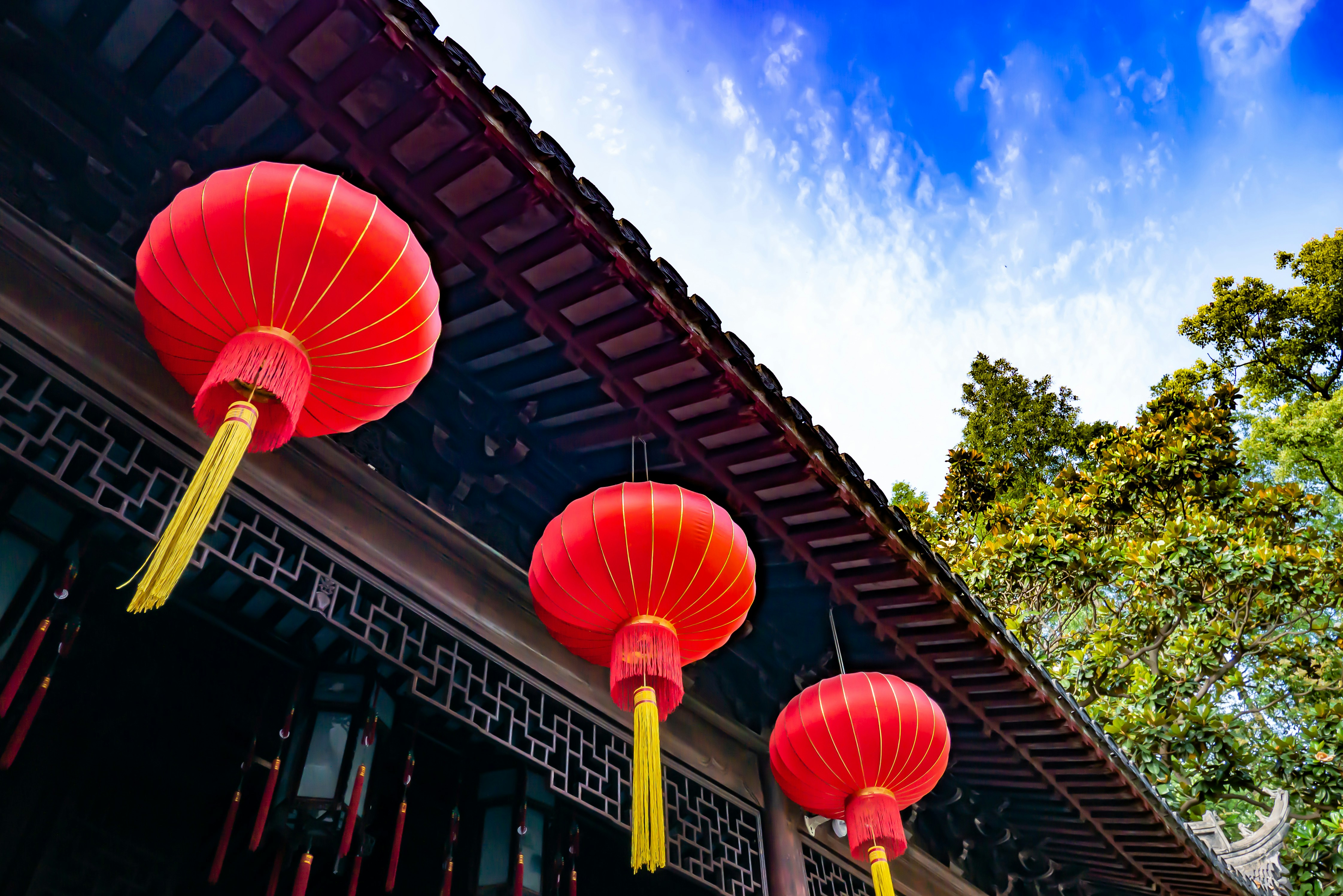 Vibrant red lanterns hang gracefully from an ornate roof, contrasting against a bright blue sky and lush greenery. The scene captures the essence of cultural celebration.