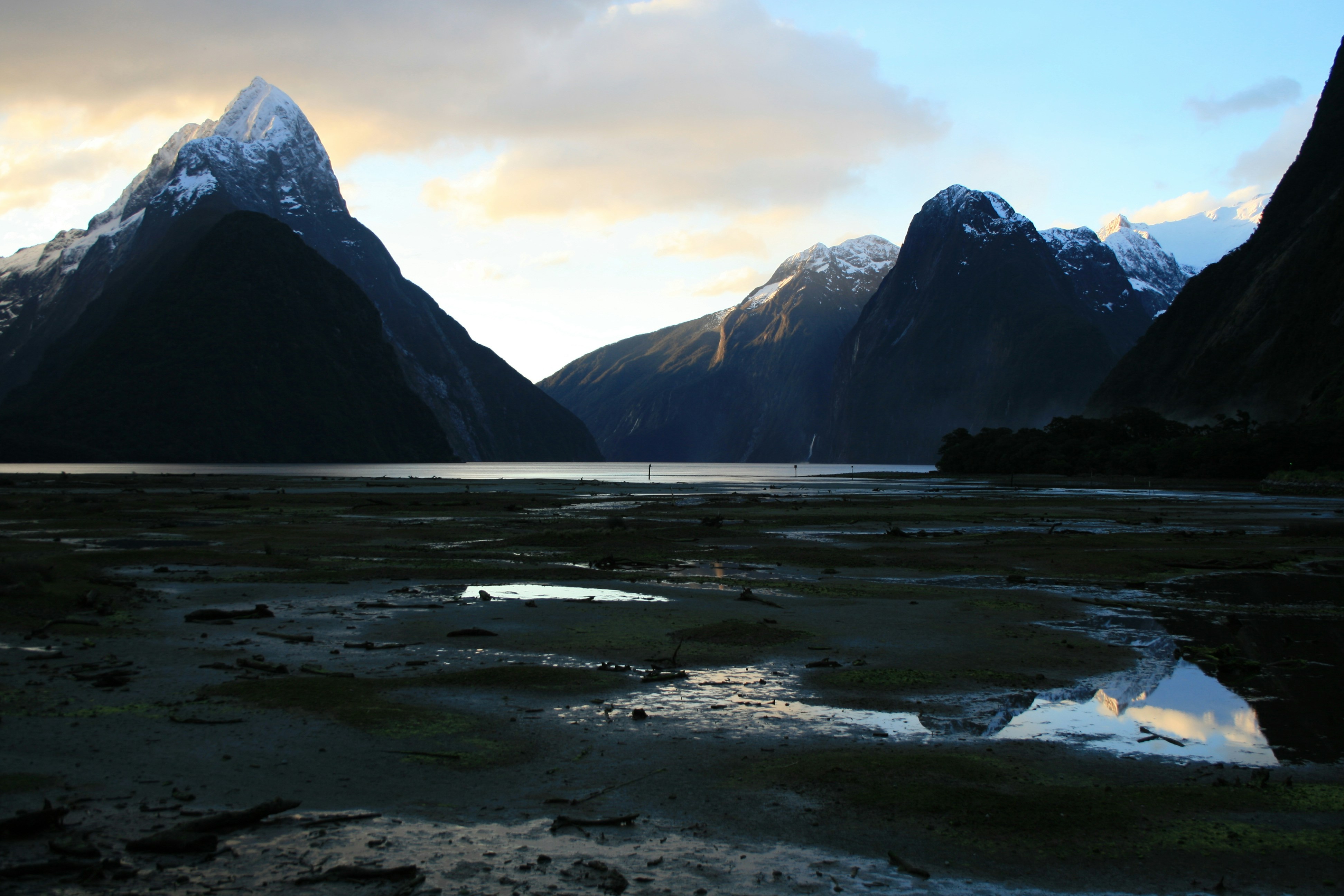 Snow-capped mountains reflected in calm water under a dusky sky.
