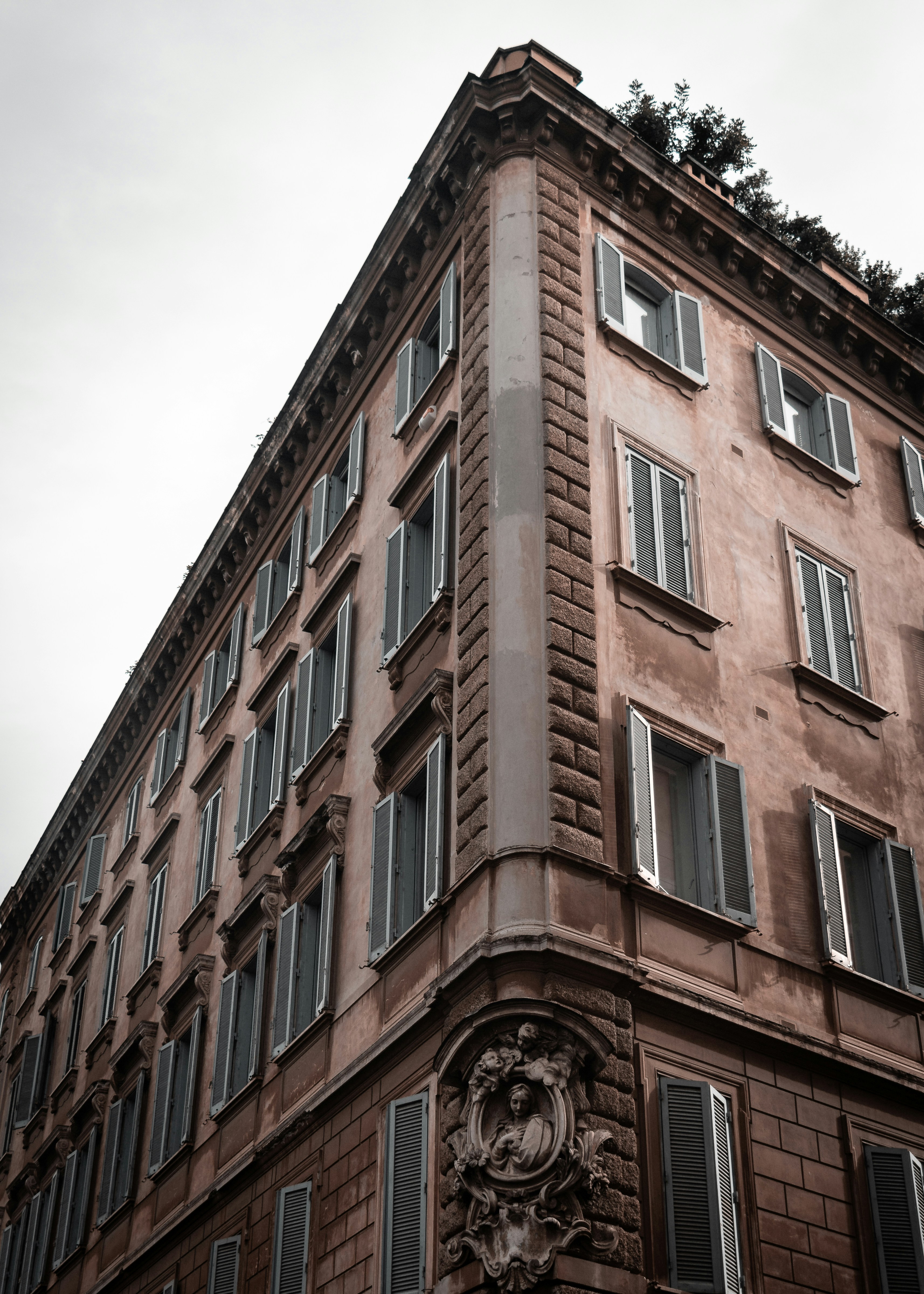 Architectural detail of a weathered building corner featuring ornate stonework and shuttered windows. A glimpse into the past captured in muted tones.