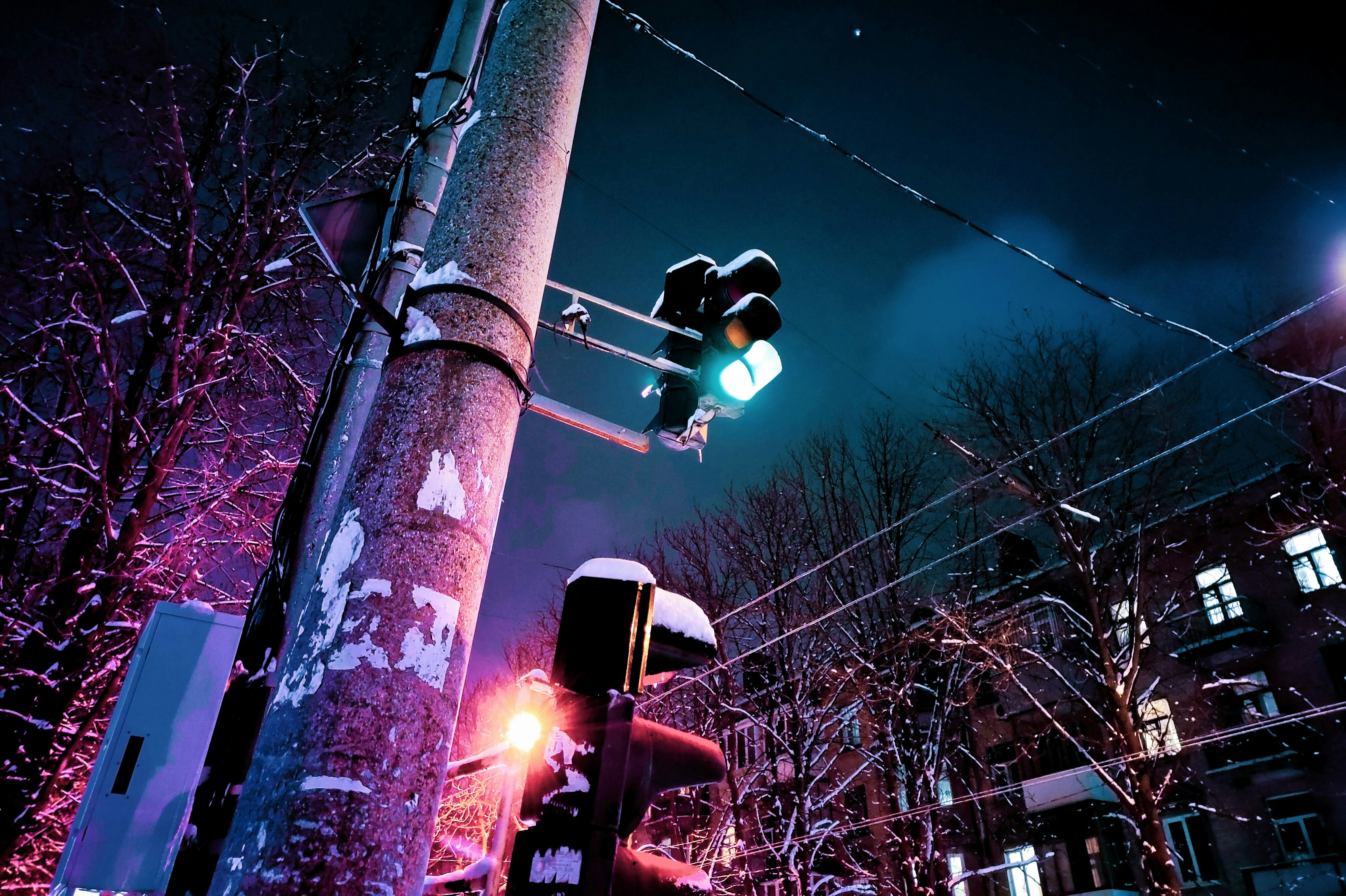 Night street scene photograph featuring a snow-dusted utility pole, glowing traffic lights, and blue-pink neon illumination.