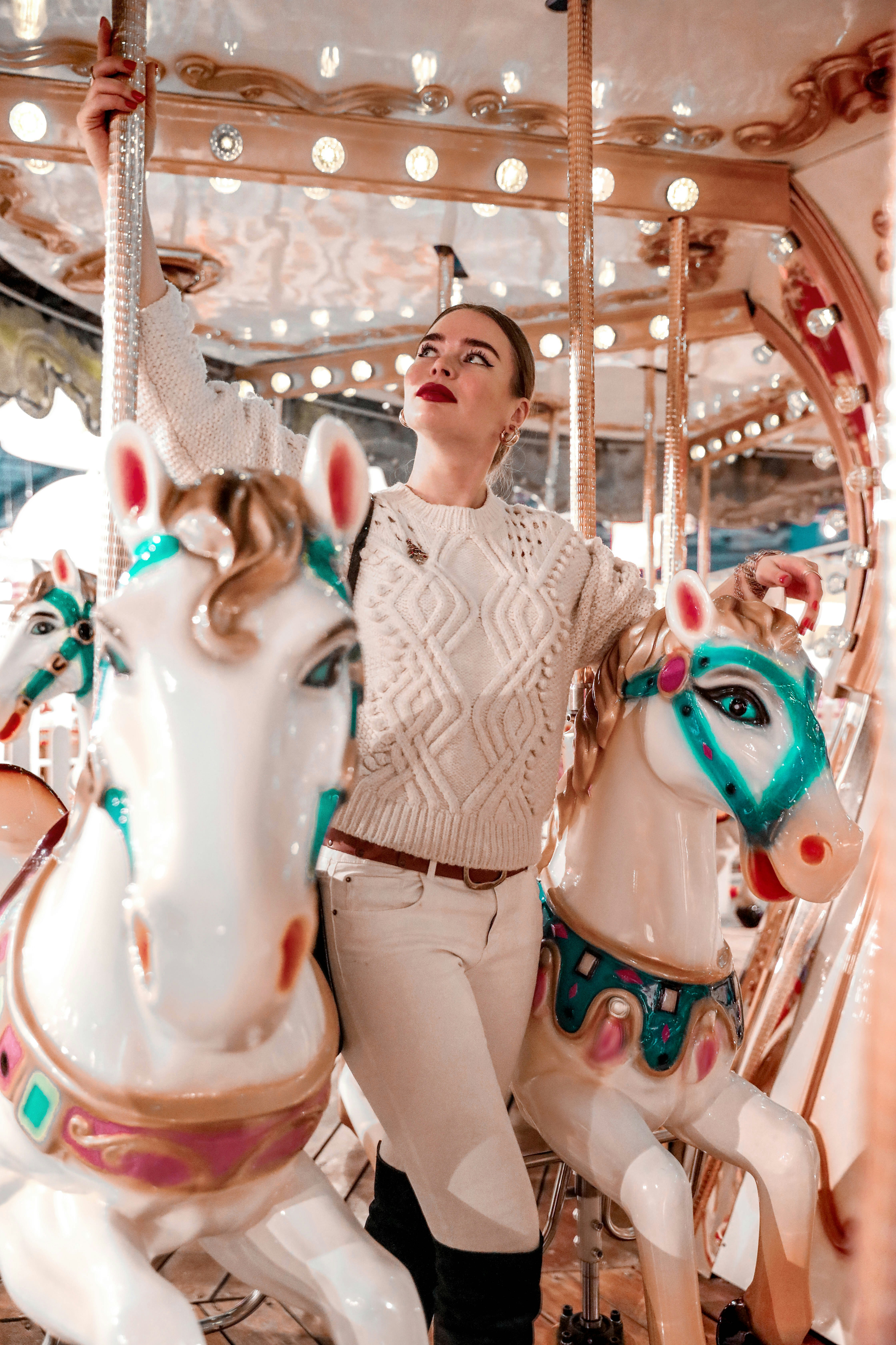 Carousel Confidence: A Woman in Knitwear Amid Carousel Horses