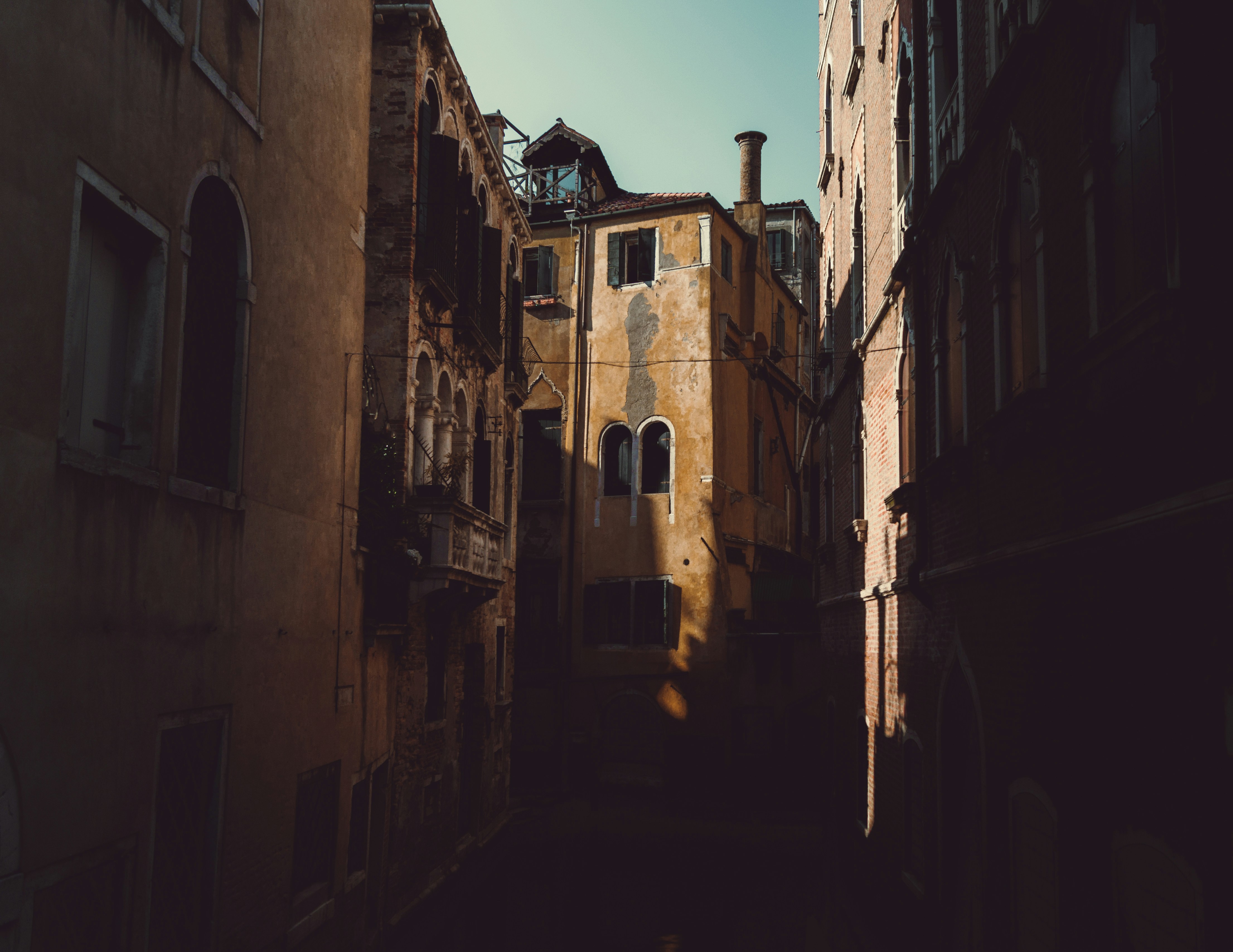Narrow canal flanked by aged buildings, illuminated by soft sunlight filtering through the architecture. A serene moment capturing the essence of Venice.
