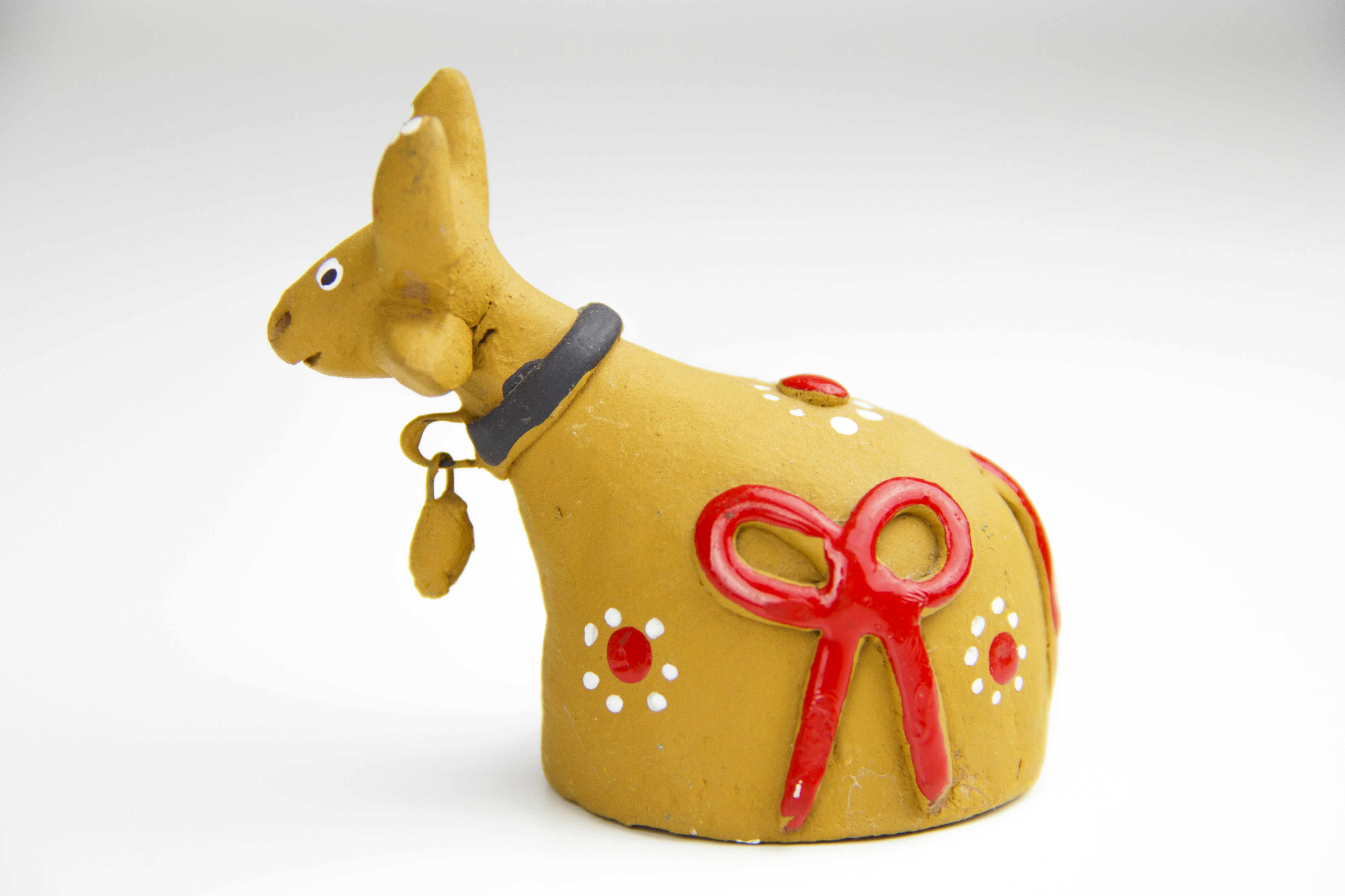 A creatively designed clay figure resembling a dog, adorned with a red bow and decorative spots. The figure exudes a playful charm.