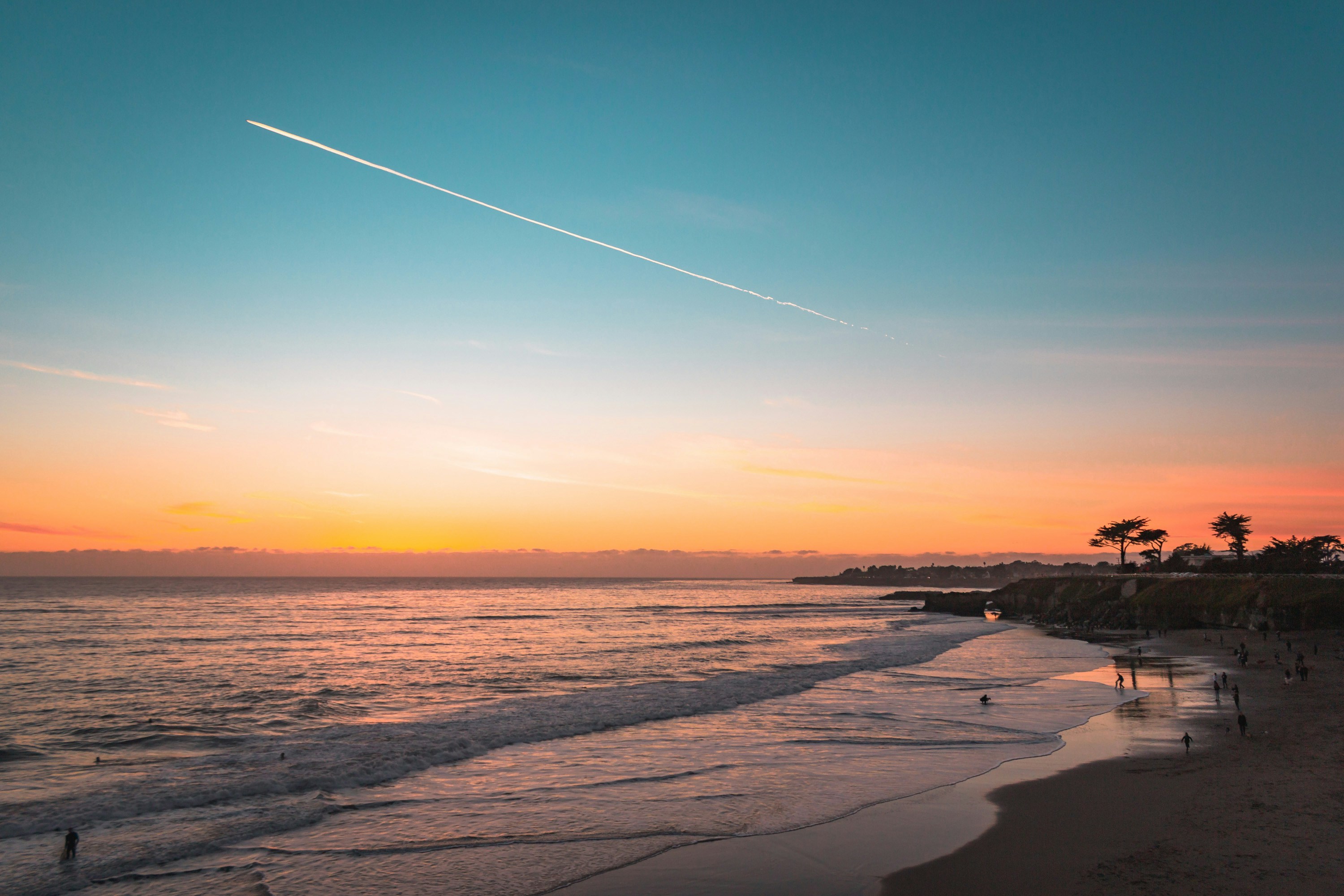 Vibrant sunset over a serene beach with silhouetted figures along the shoreline.