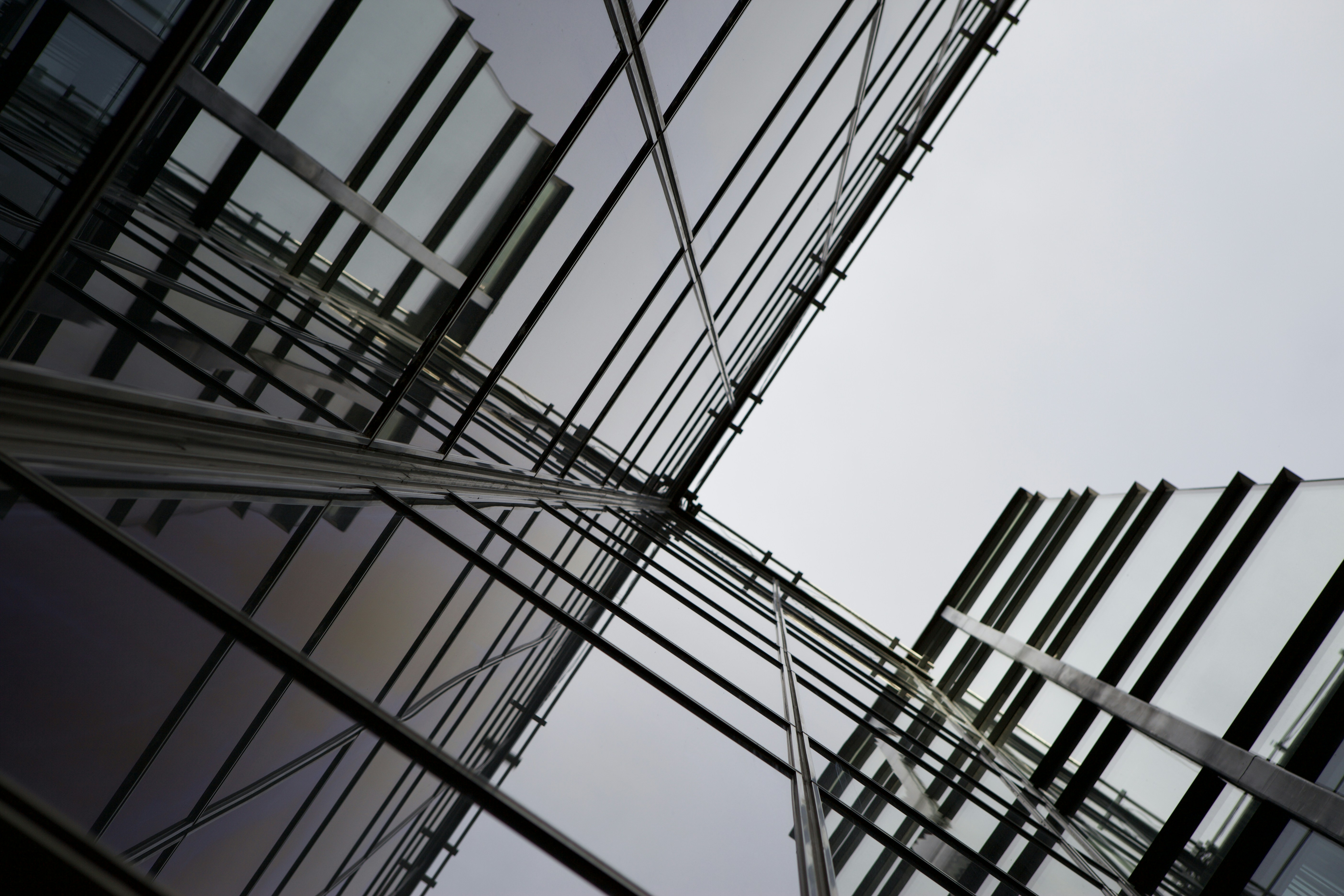 Geometric reflections of a modern glass building frame the cloudy sky.