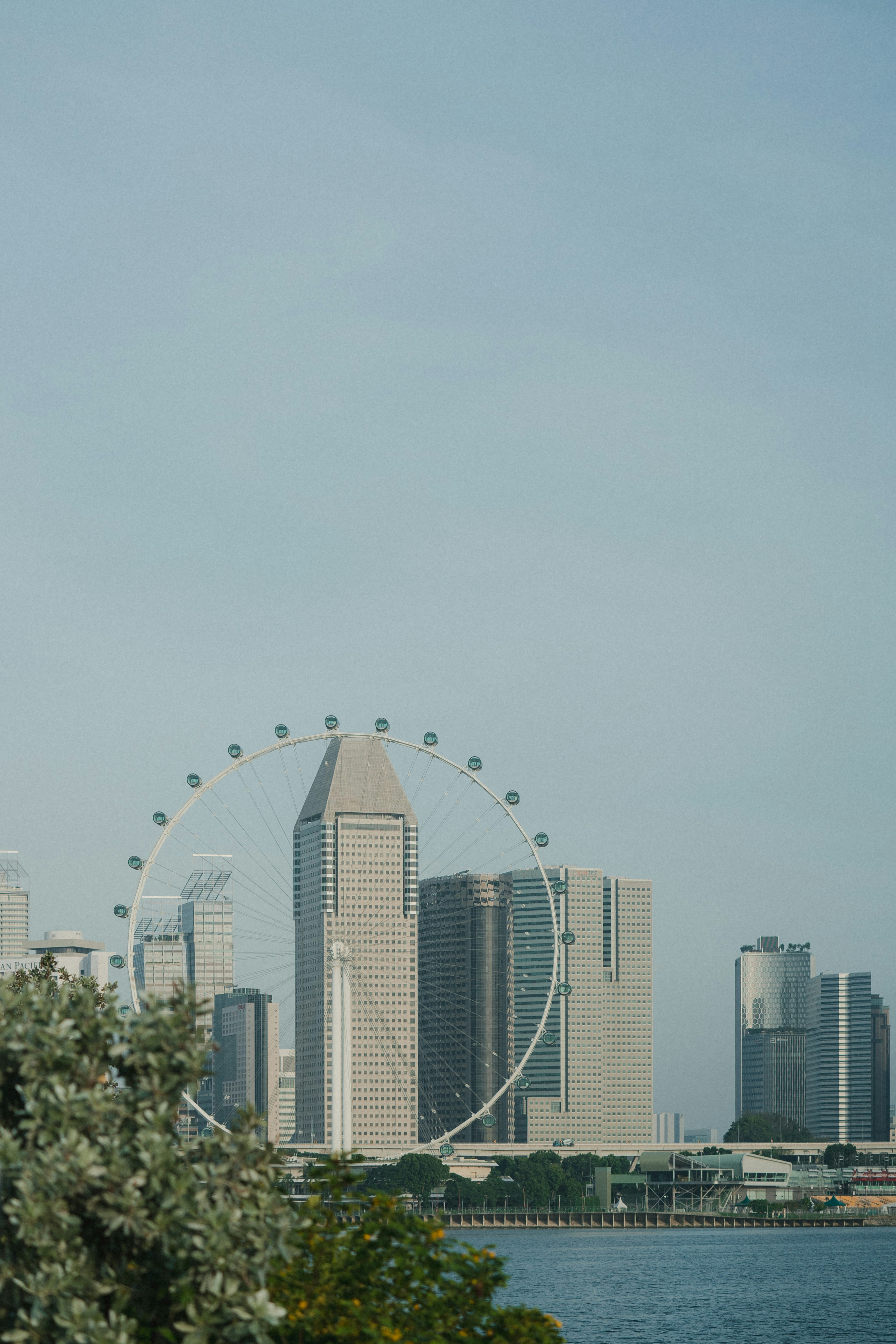 A modern skyline featuring a prominent Ferris wheel against a backdrop of skyscrapers, highlighting urban architecture and leisure. 