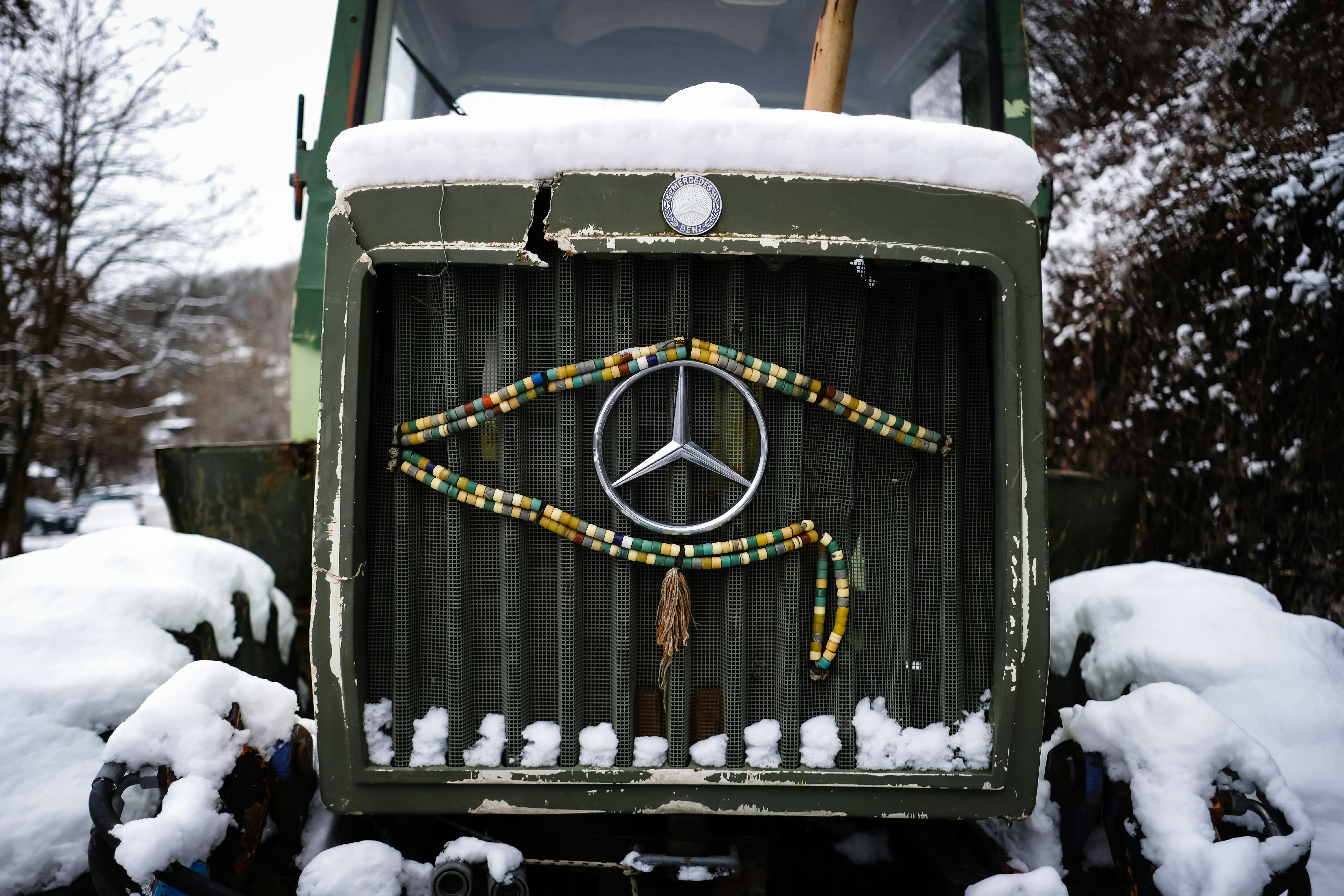 Beaded charm draped over a snow-dusted Mercedes-Benz front grille