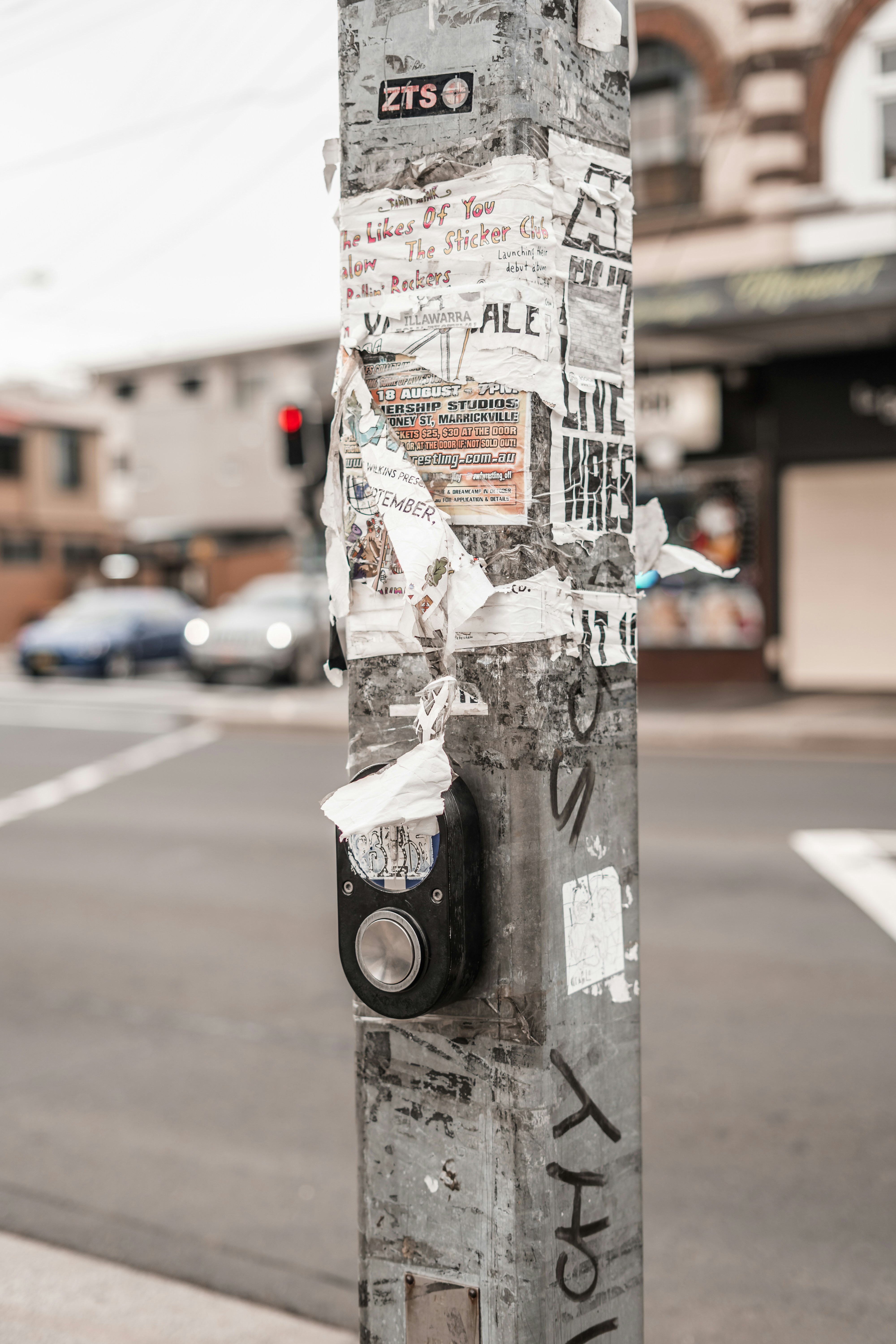 A weathered street pole adorned with various flyers and stickers, juxtaposed against a blurred urban backdrop. The scene captures the essence of city life and its transient nature.