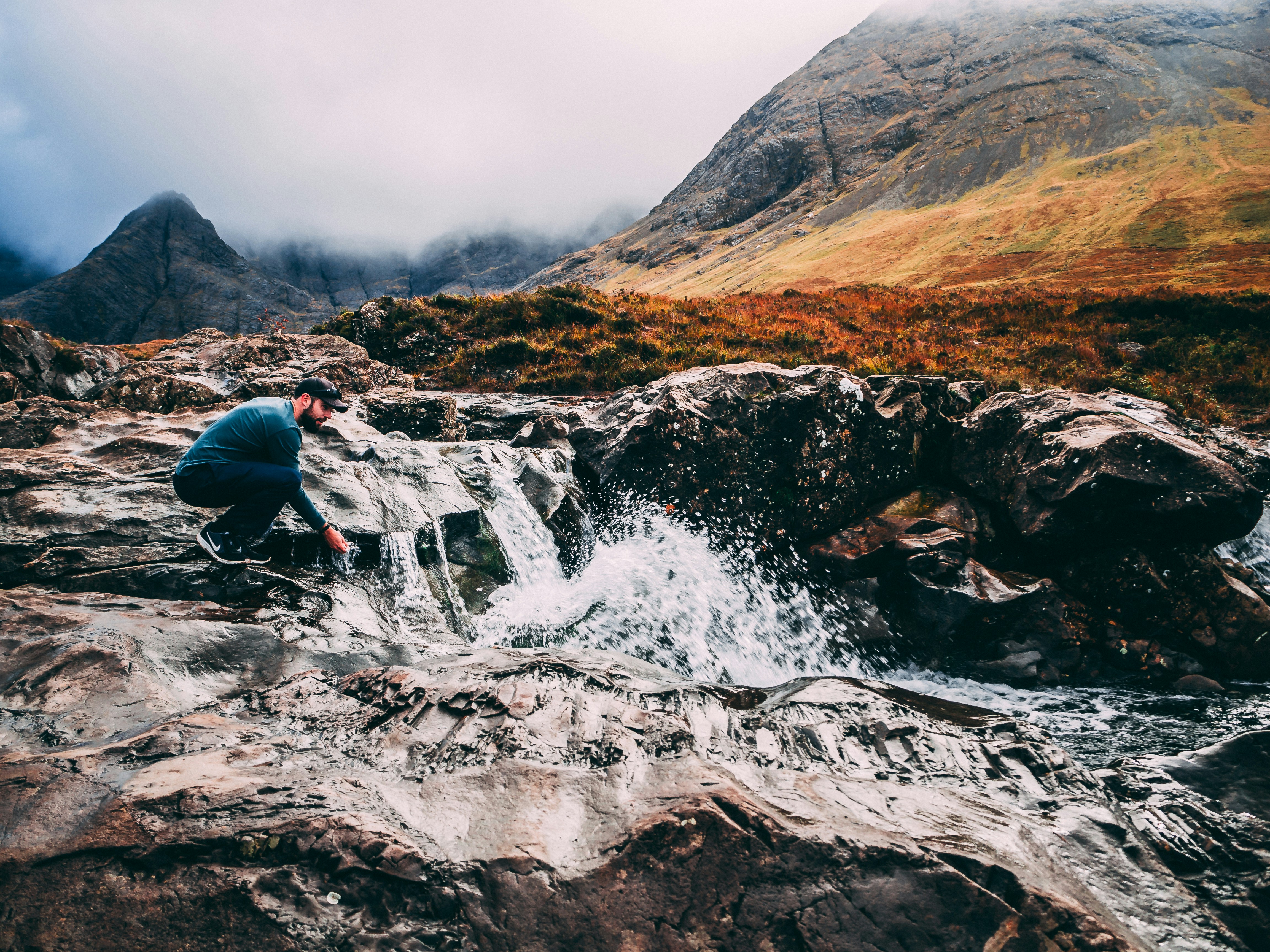 man wearing black shirt sitting near flowing water during daytime