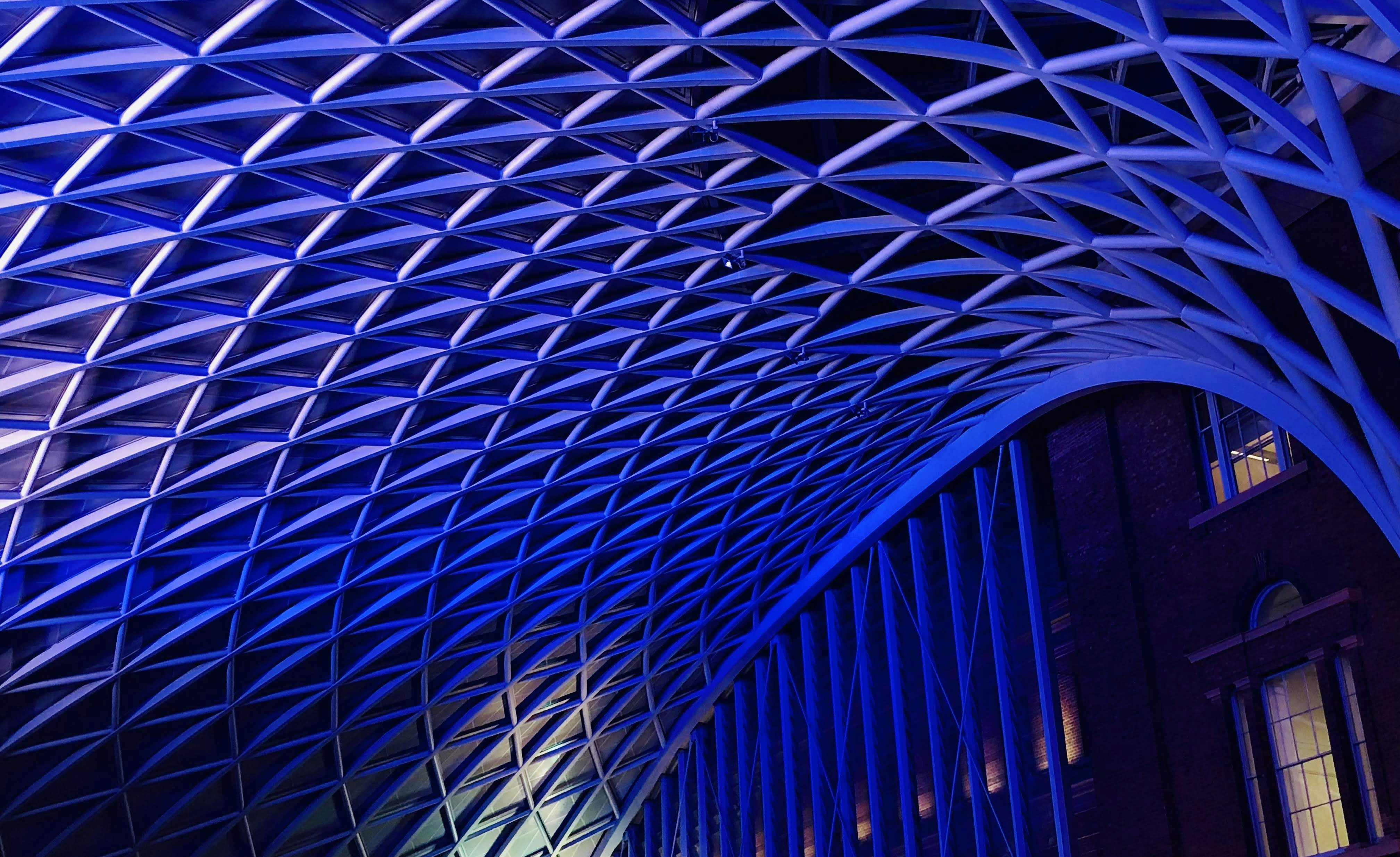 Intricate blue lattice structure of a modern architectural canopy illuminated at night, contrasting with the brick facade below.
