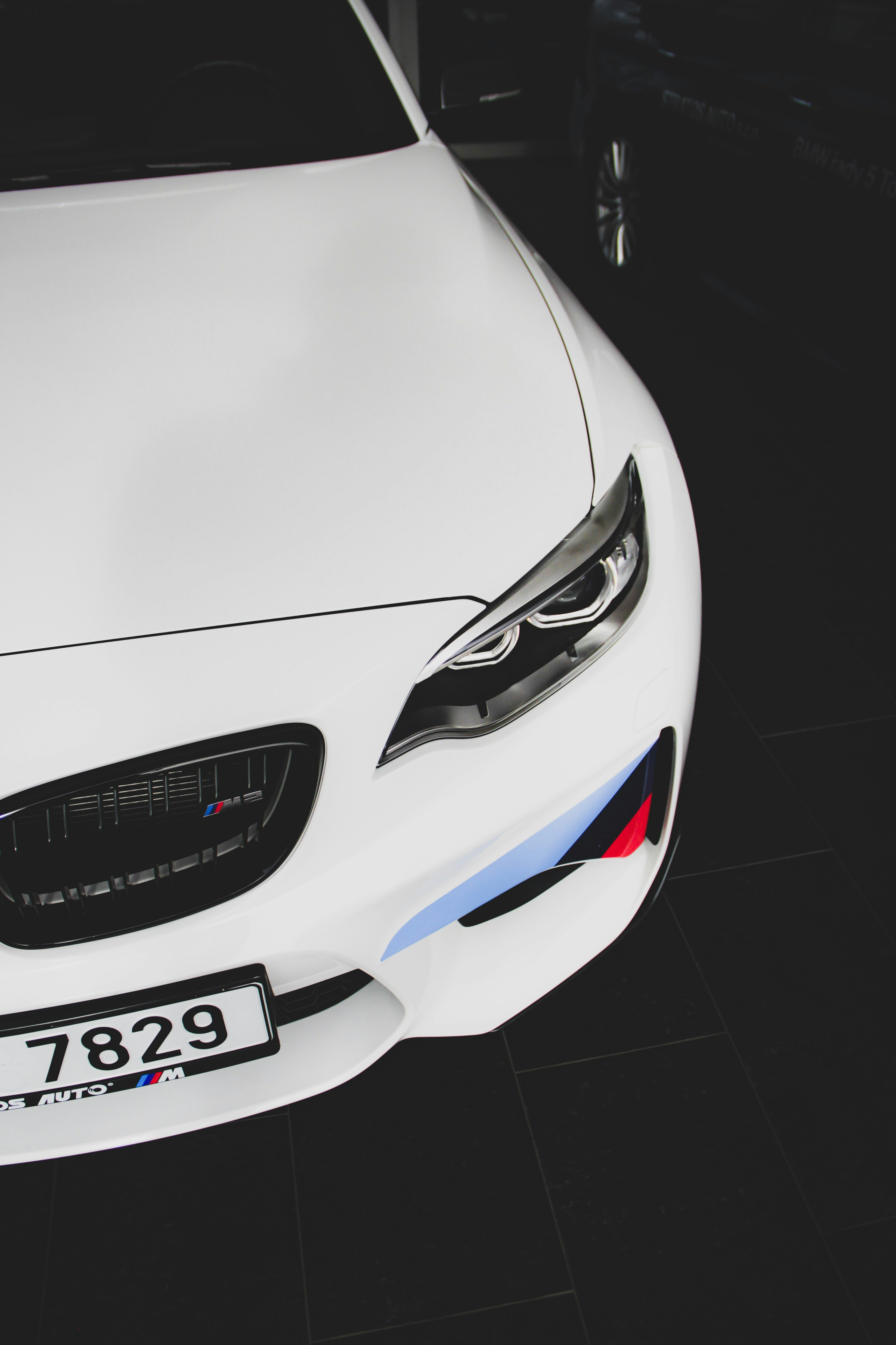 Close-up view of a sleek white sports car, showcasing its aerodynamic lines and distinctive headlights. The vehicle's branding and design elements highlight its performance pedigree.